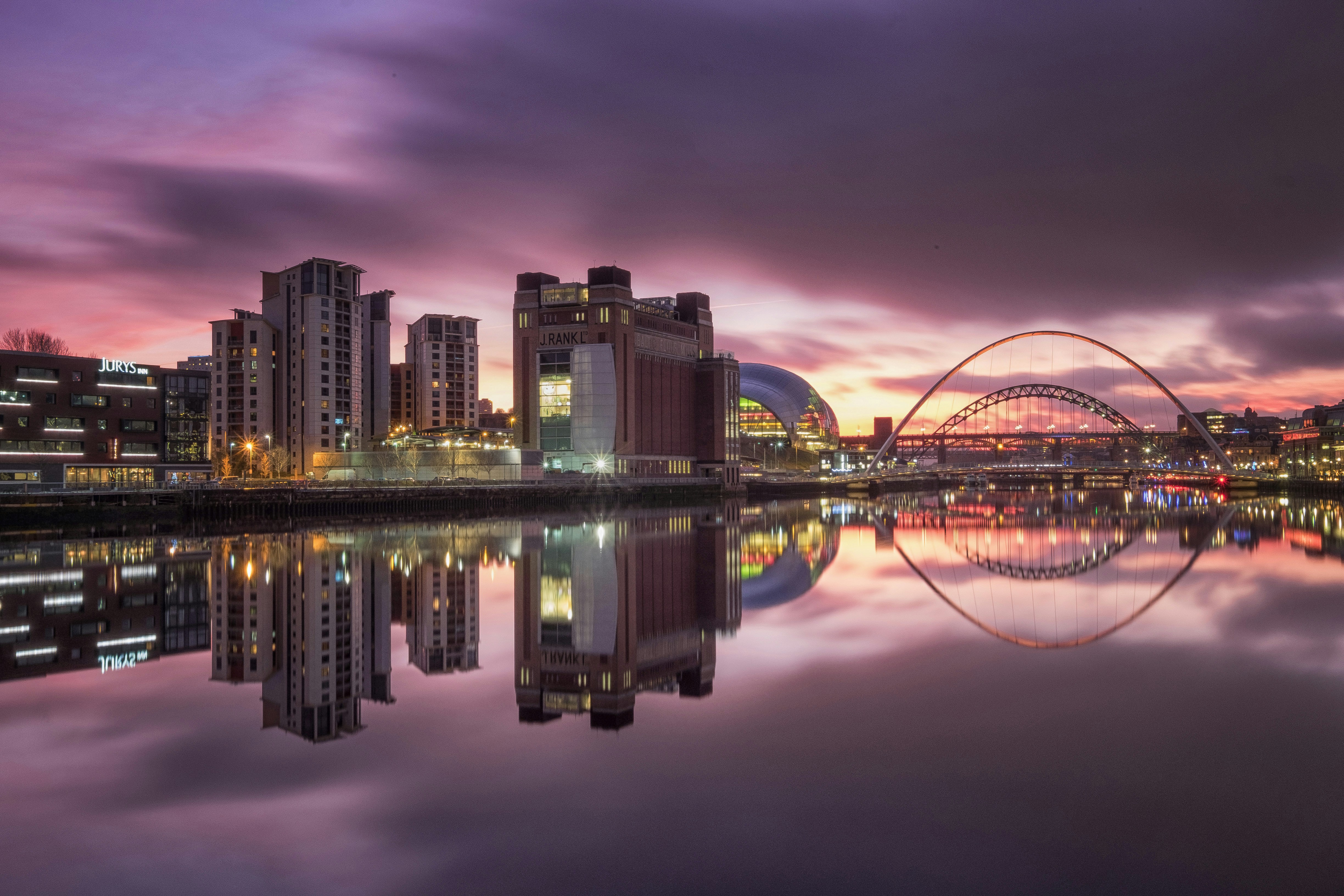 City skyline reflected in calm waters during twilight, showcasing modern architecture and a vibrant sky.