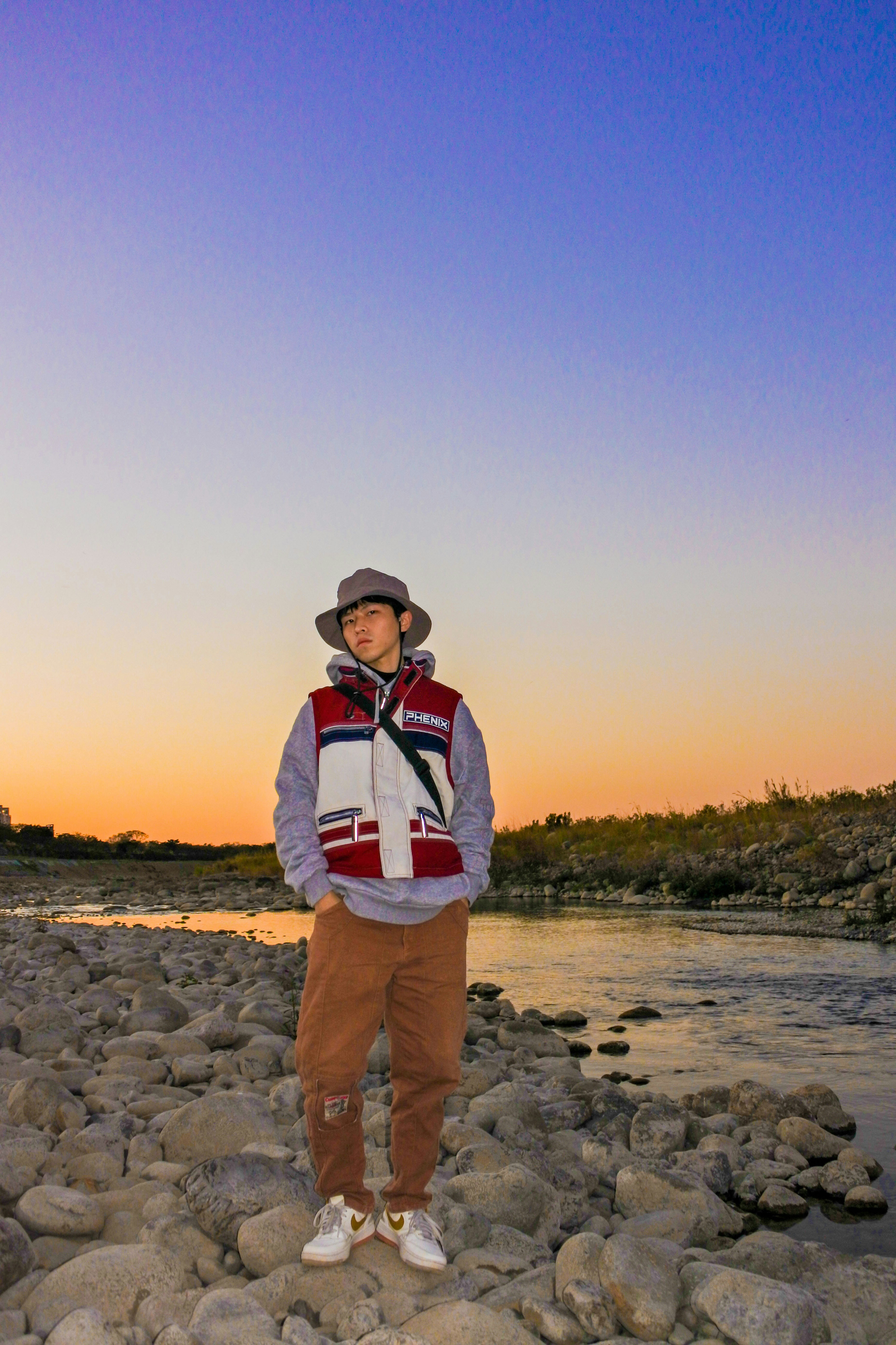 Sunset Pebble Shore: A Casual Explorer in Red-White Vest