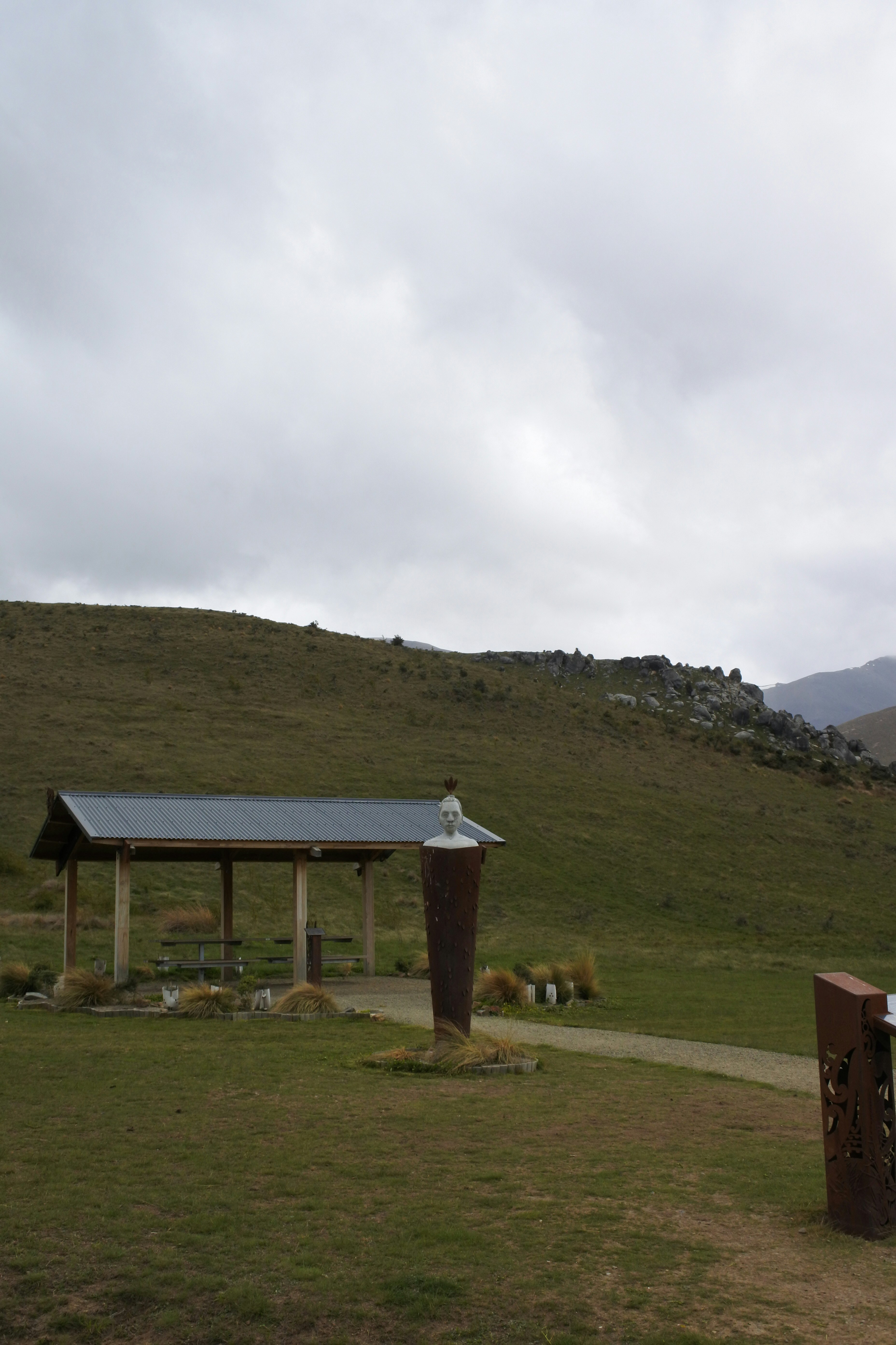 Stone Head on a Rusty Pillar Overlooks a Quiet Hilltop Shelter