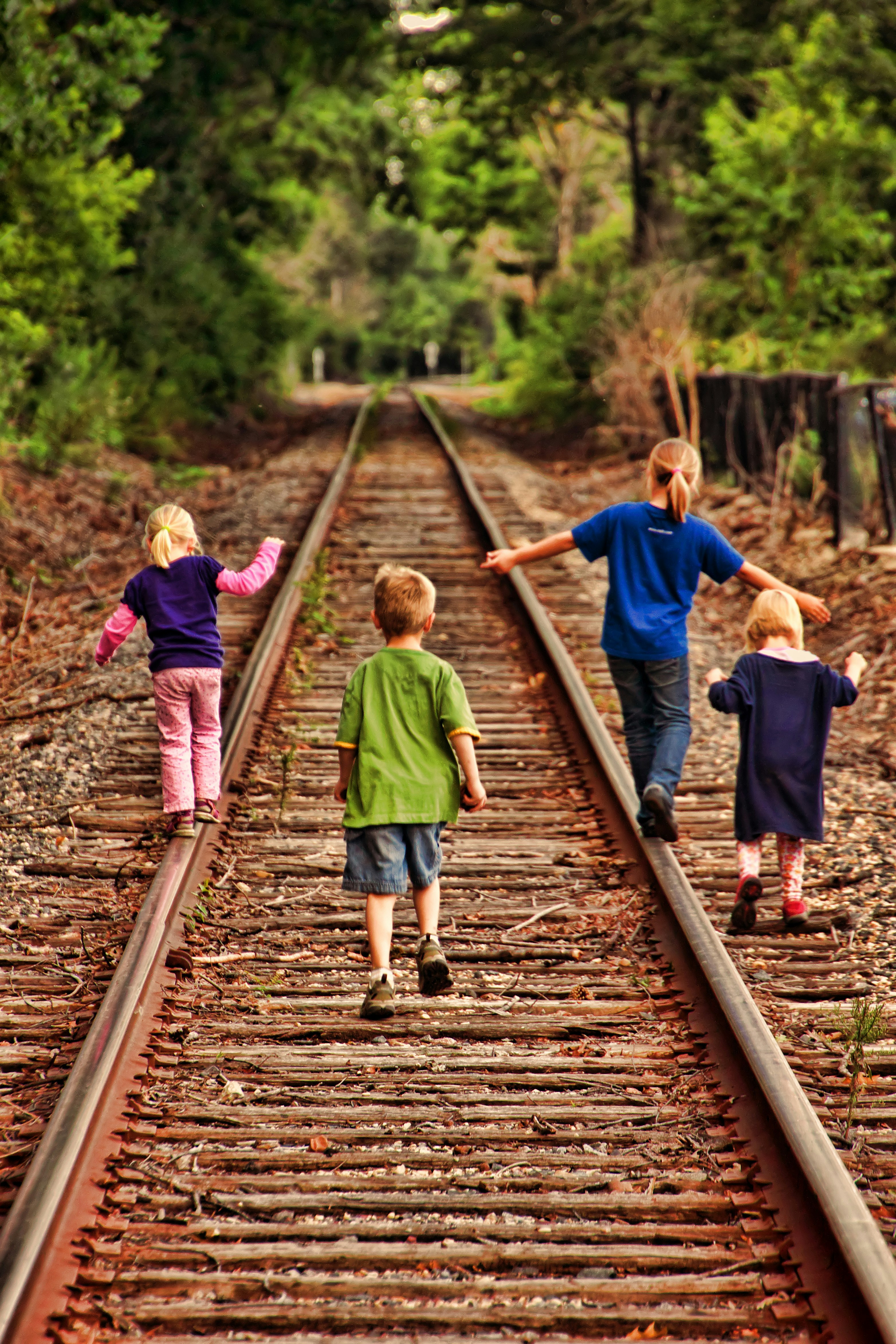 Four children walk down railroad tracks.