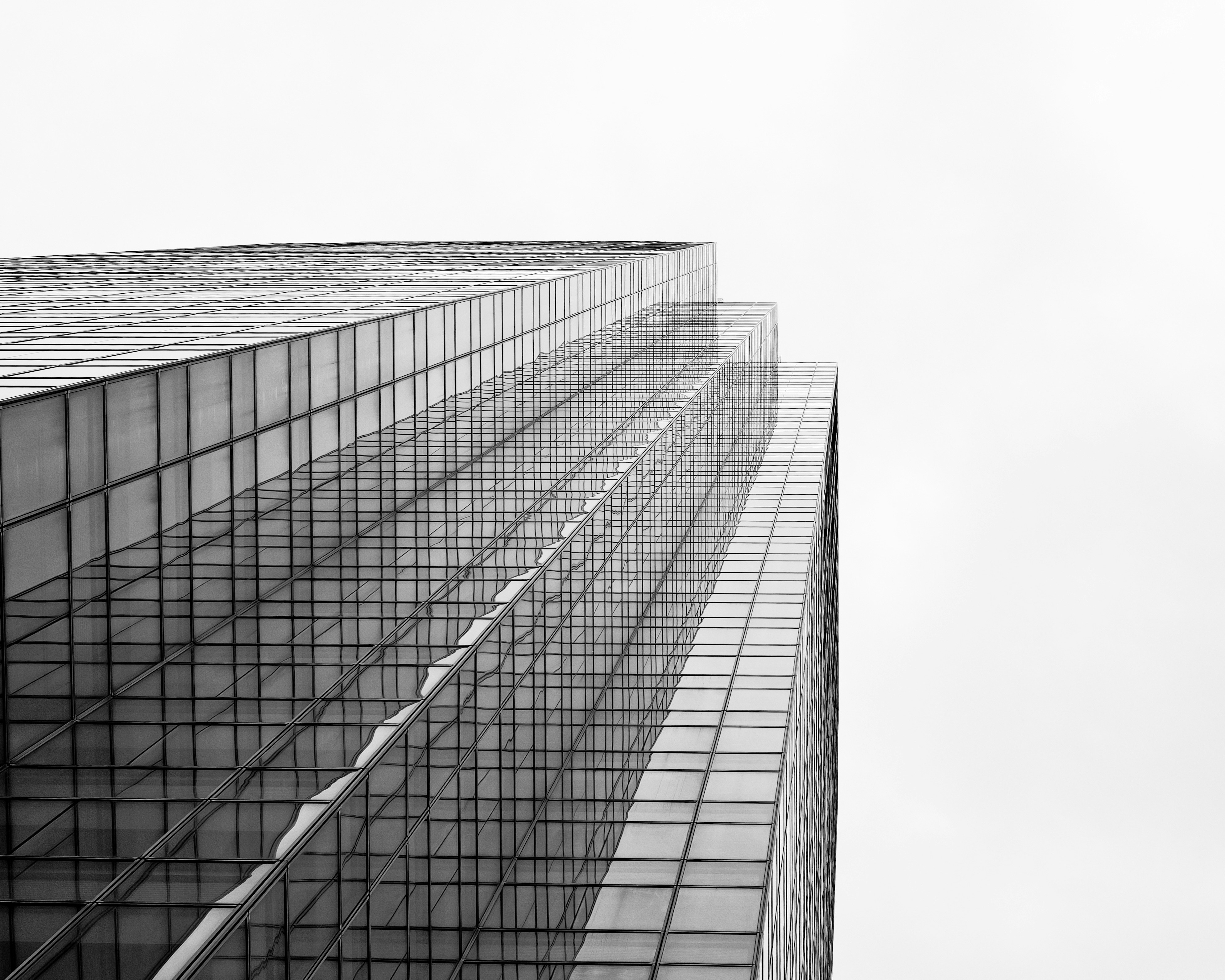 Abstract architectural composition showcasing a tall building's reflective glass facade against a cloudy sky.