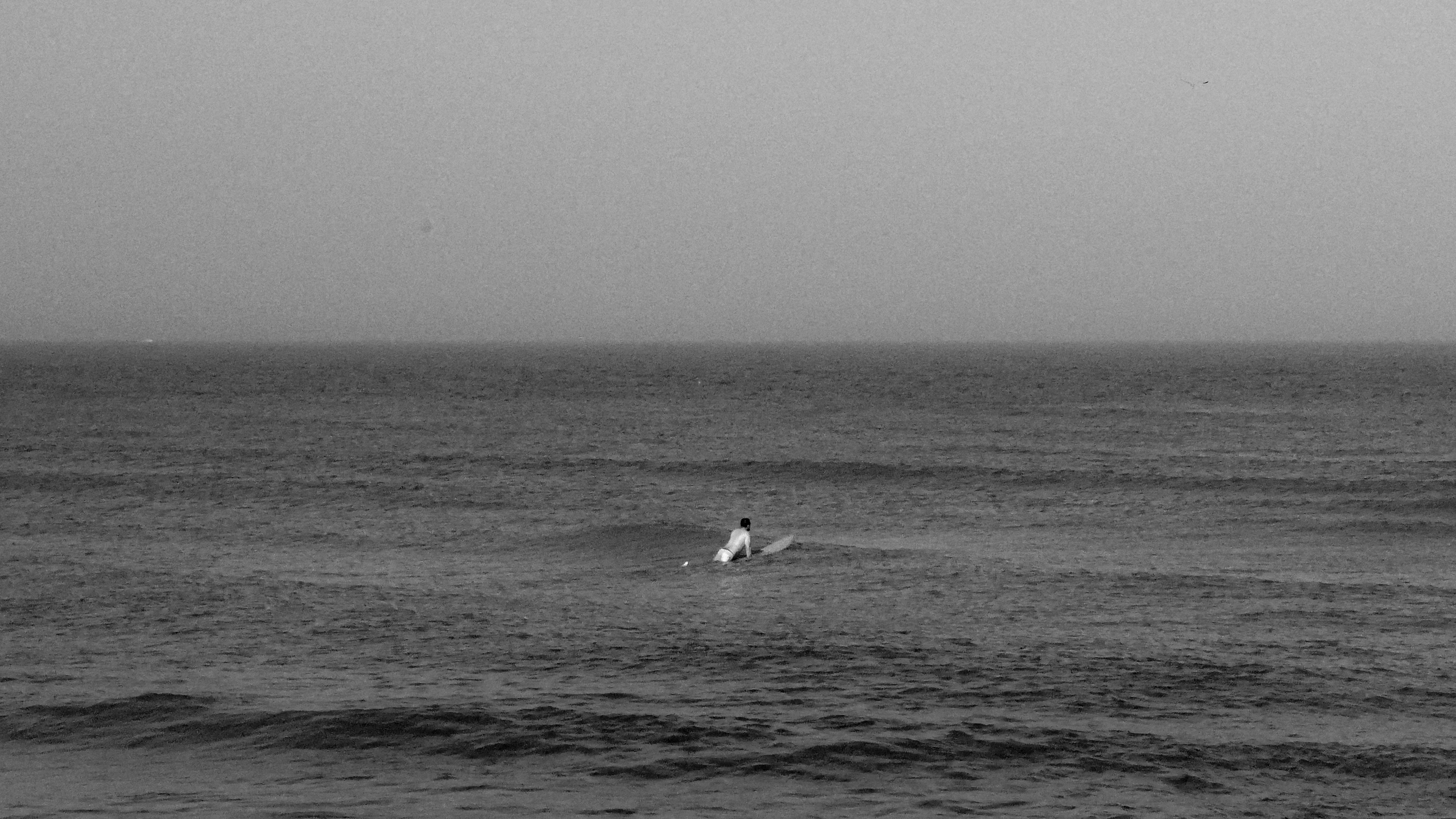 A lone surfer waits for waves in the ocean.