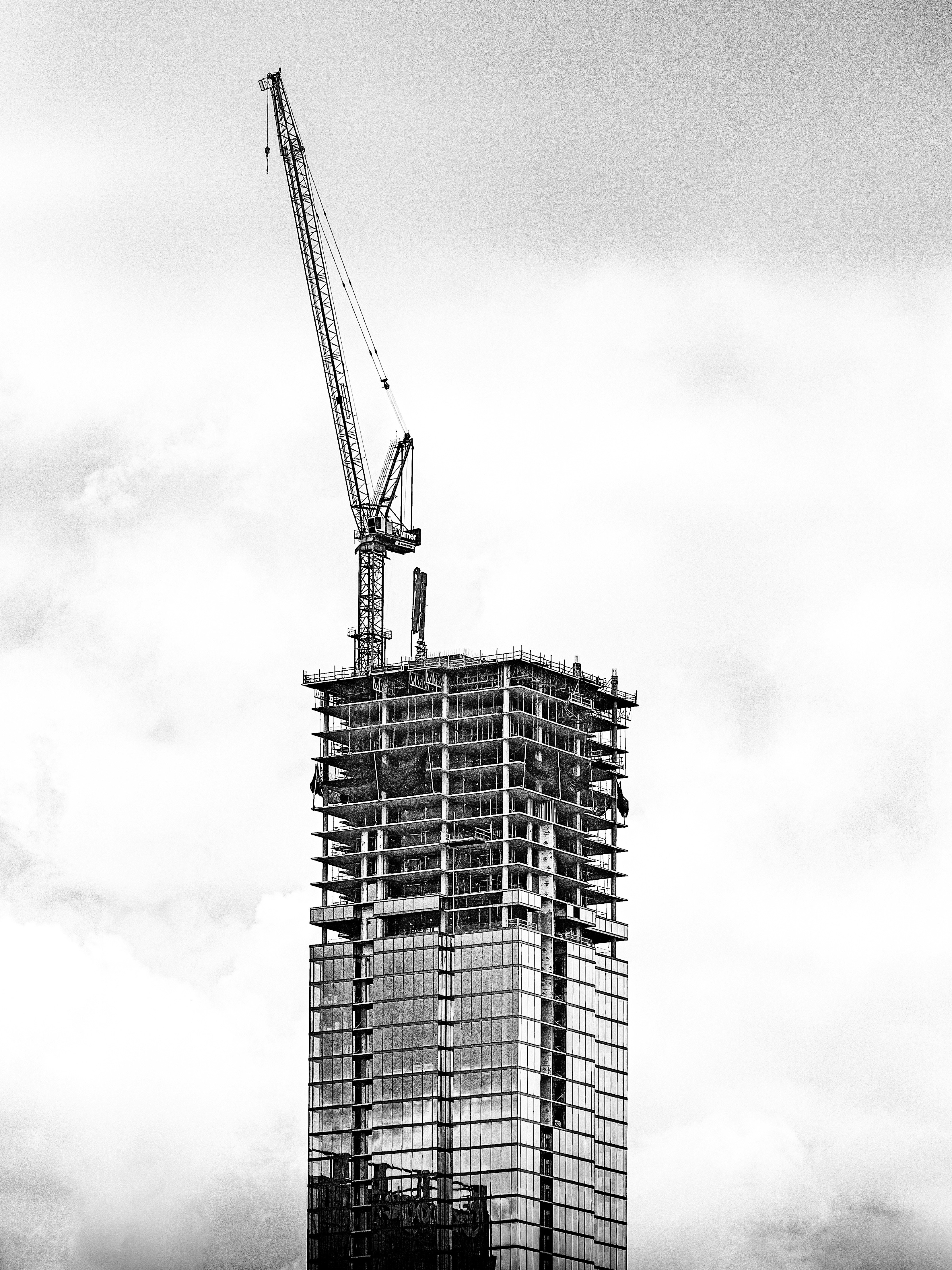 A construction site featuring a partially completed skyscraper with a crane against a cloudy sky.