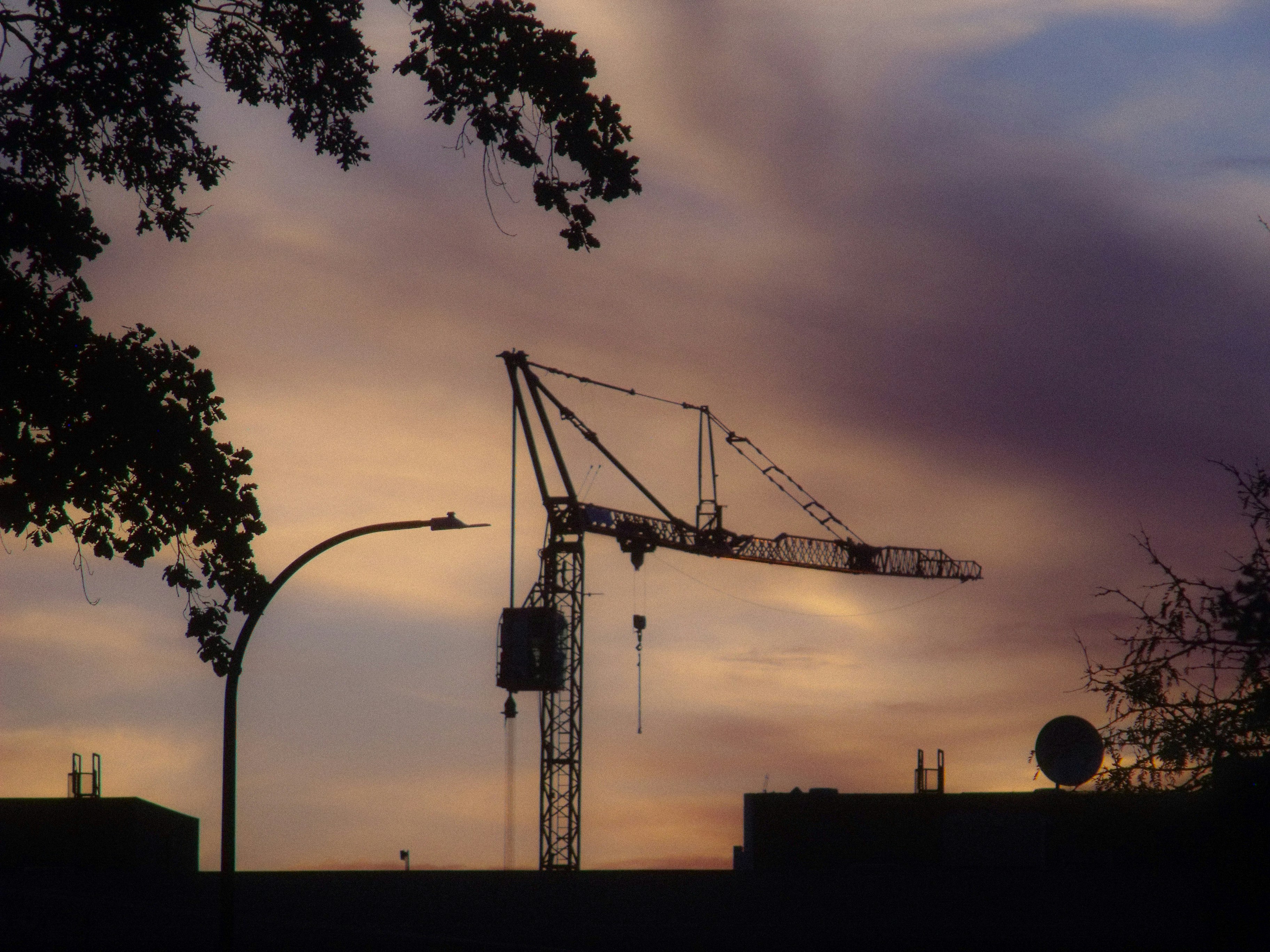 Construction crane silhouetted against a colorful sunset sky.