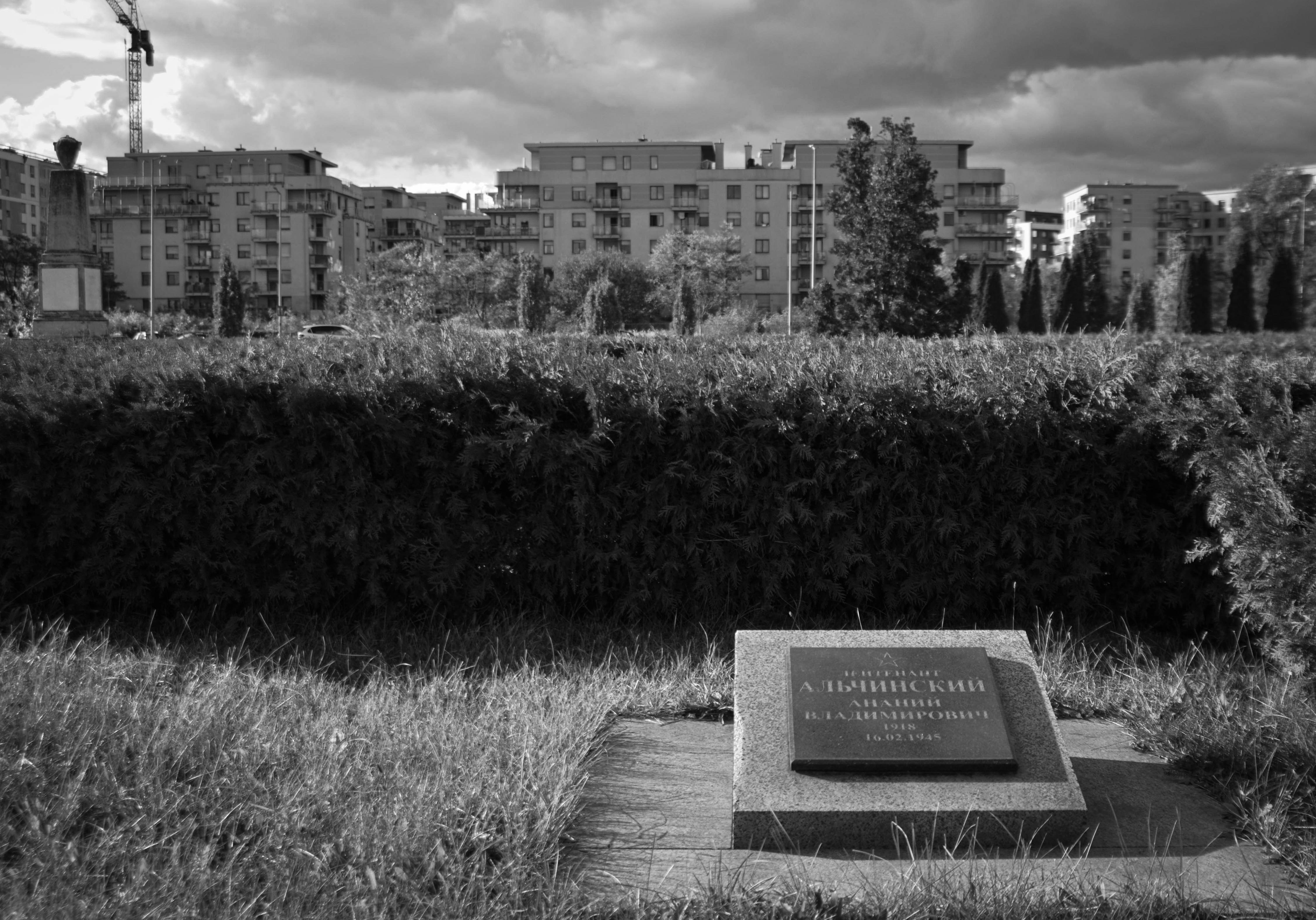 Memorial plaque set against a backdrop of modern buildings and greenery. The scene captures a blend of nature and urban life.