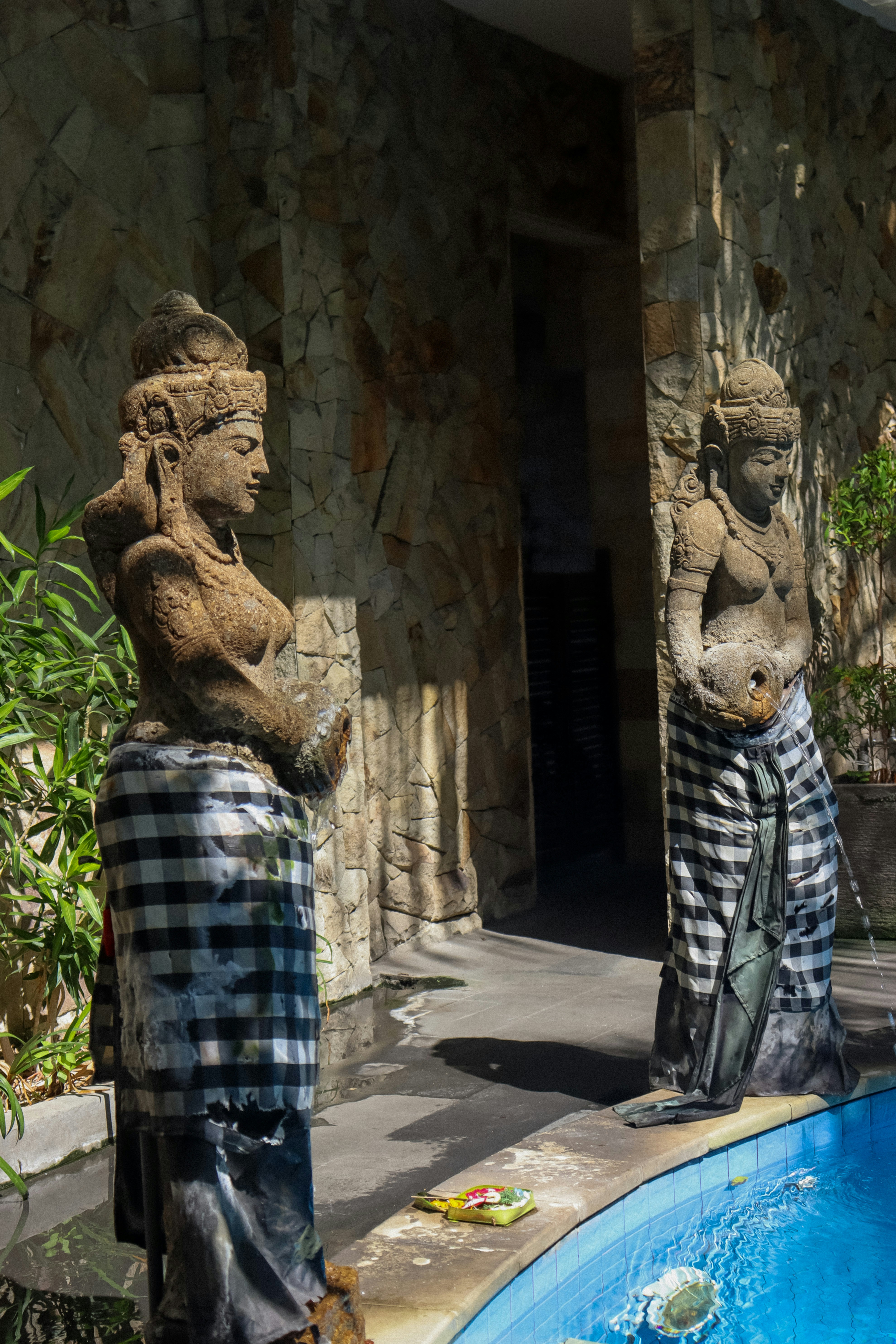 Guardian statues by the pool: stone figures in a sunlit courtyard