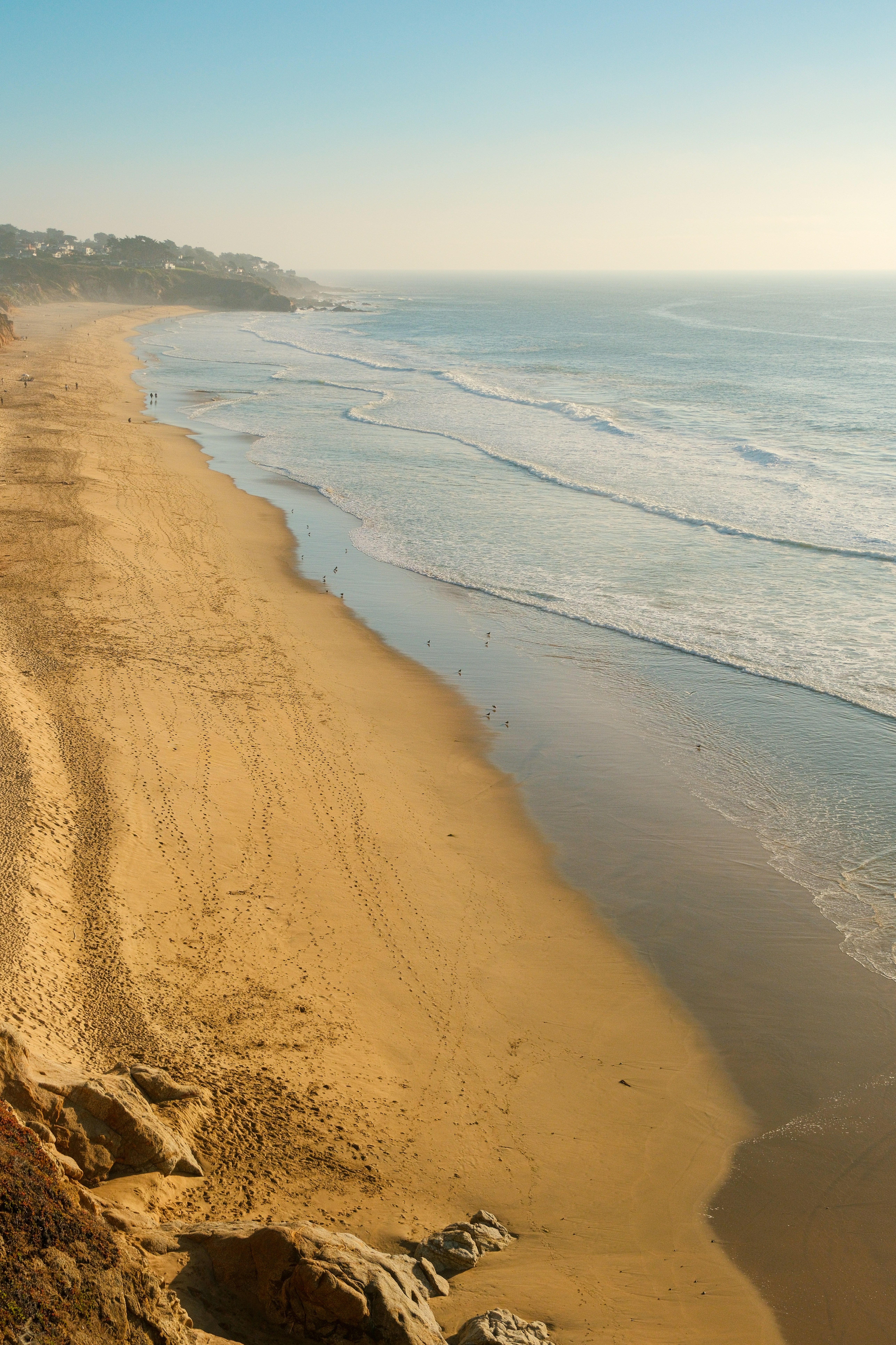 Golden sandy beach stretching along the coastline with gentle waves lapping at the shore under a clear sky.