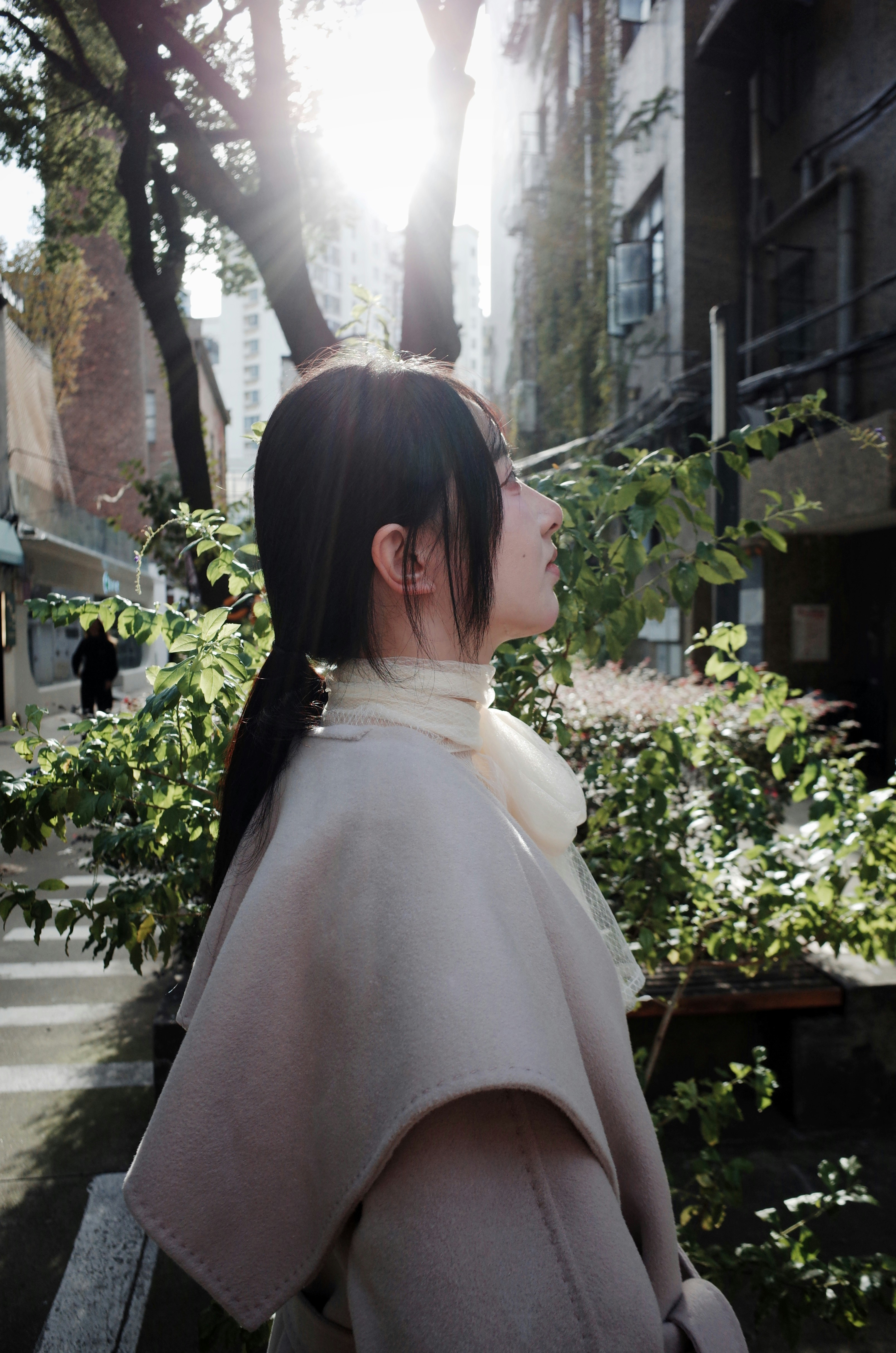 Young woman in a coat looks towards sunlit trees