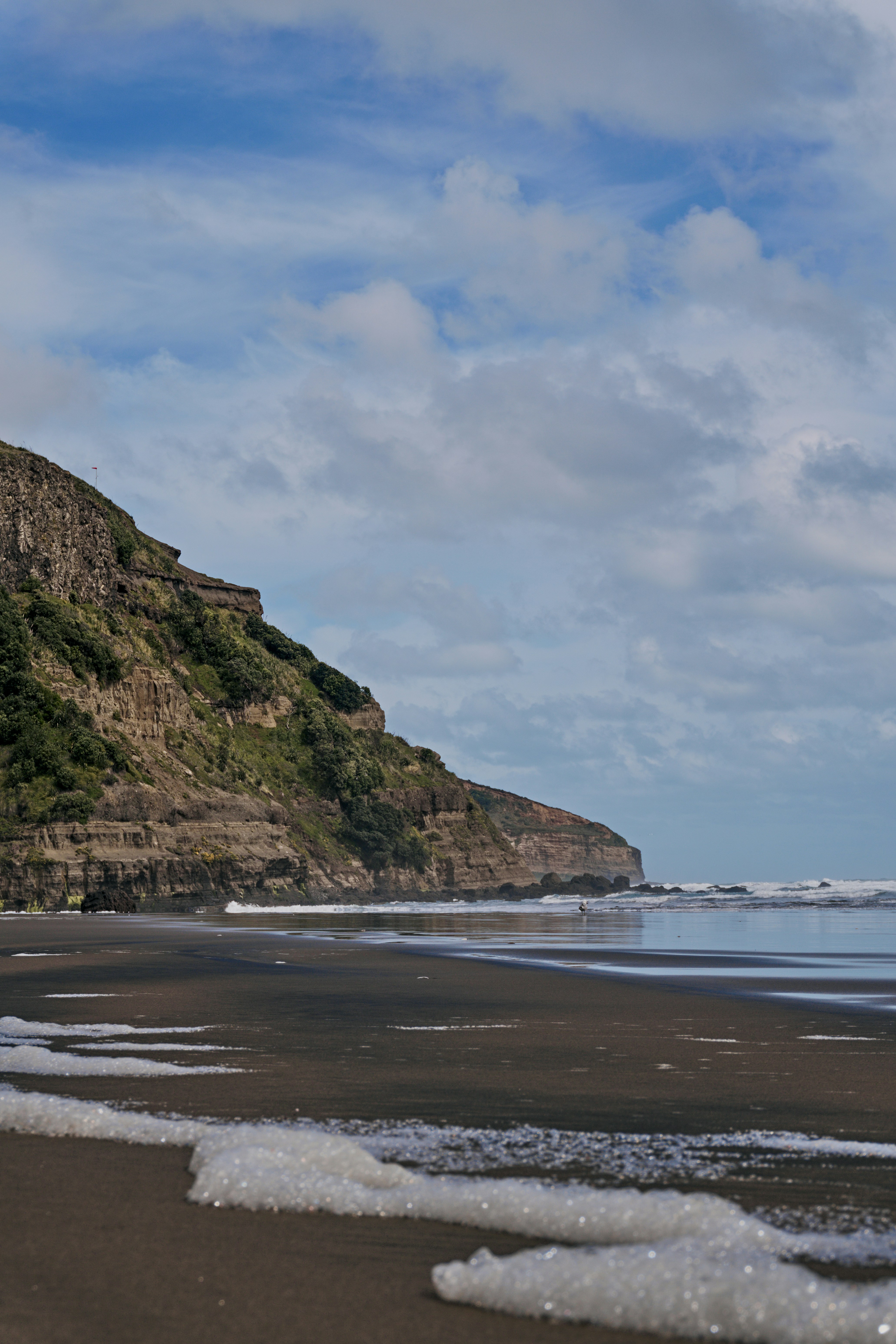 Rocky cliff overlooking a sandy beach with ocean waves.