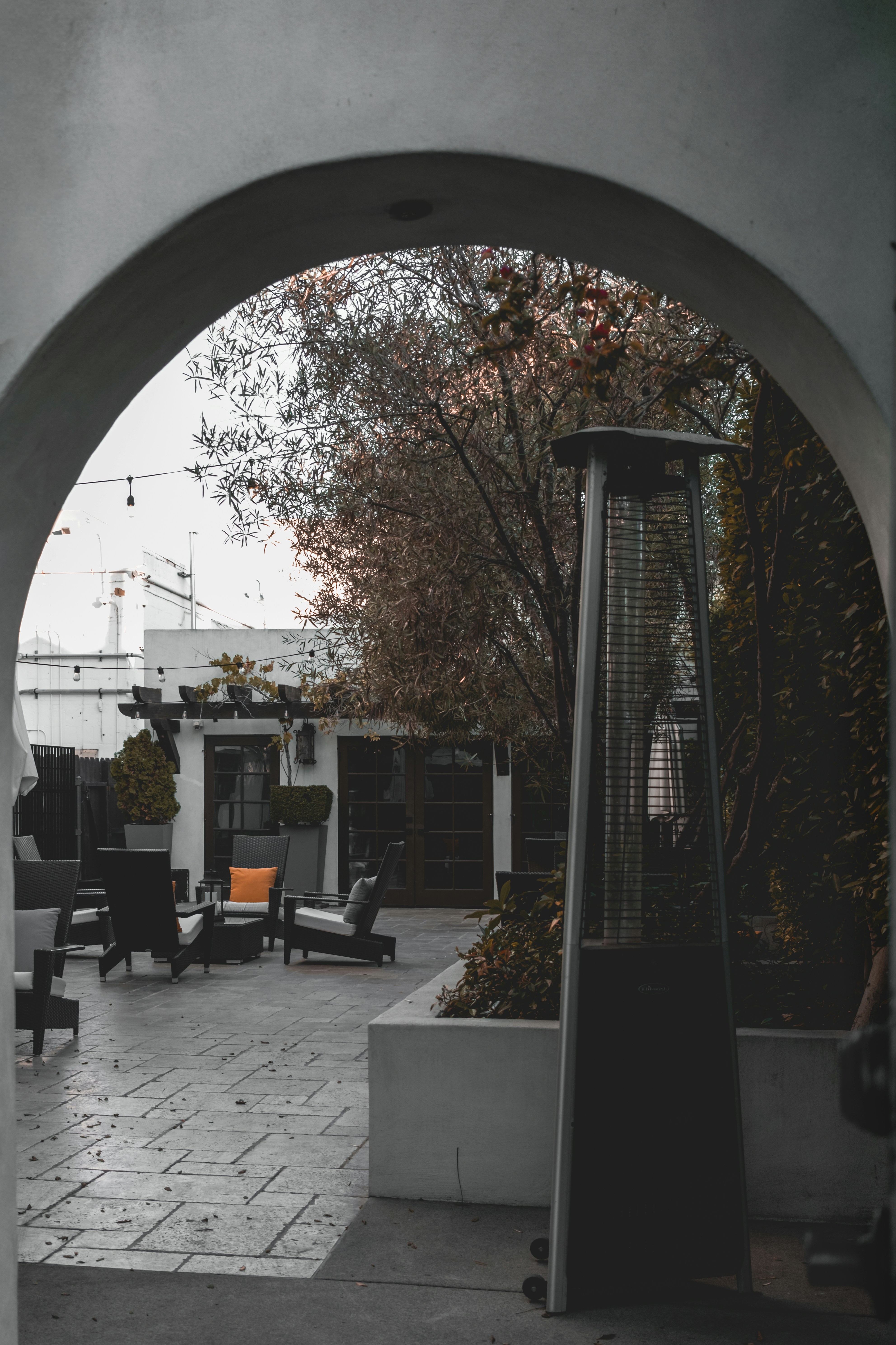 “Still between walls” | Outdoor patio seating area with heater and trees