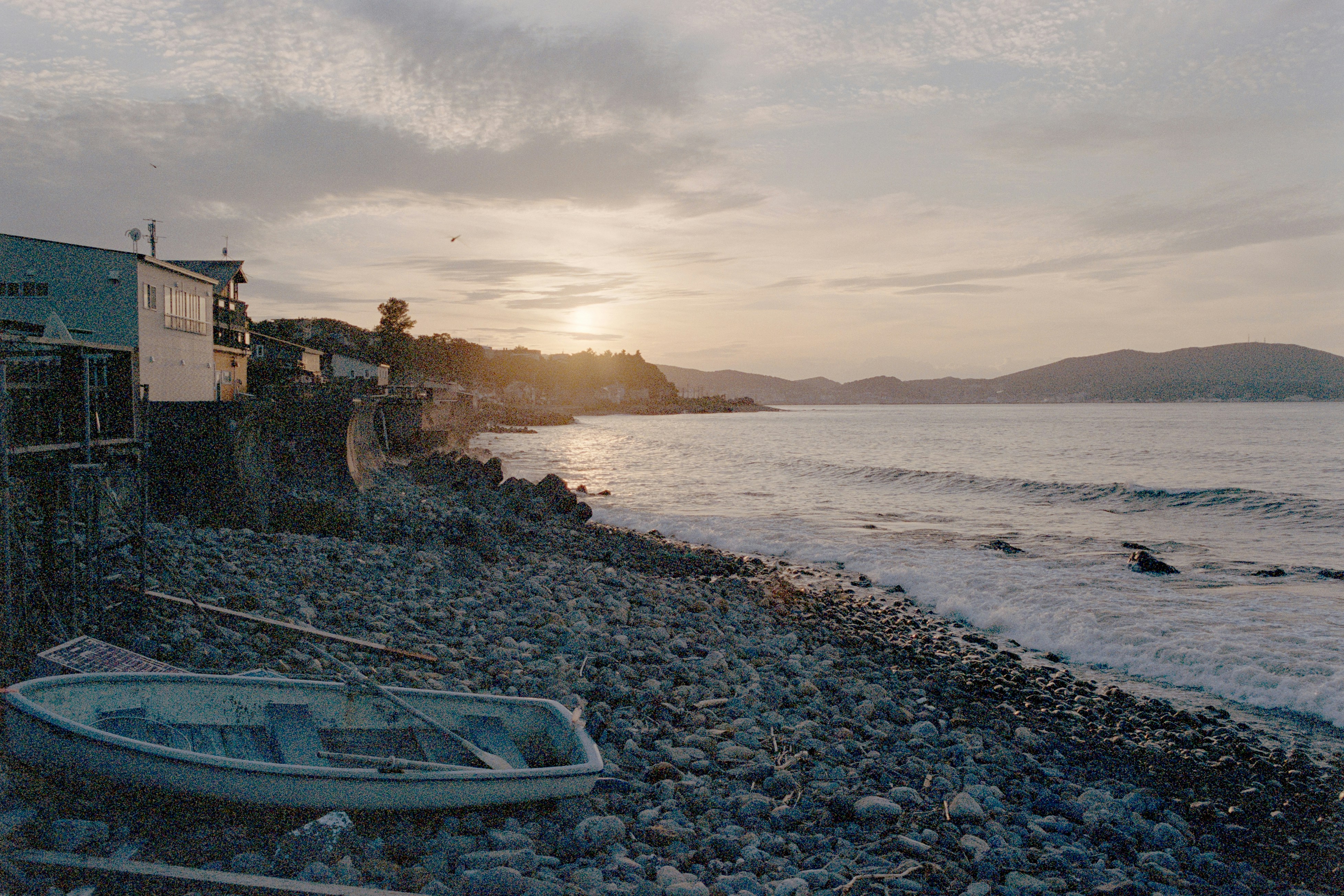 🎞️ Kodak Professional Portra 400｜🧪 Fuji Hunt C-41｜🖨️ EOS R6 + RF 100mm f/2.8L Macro｜📷 Canon New F-1 + FD 35mm 1:2 S.S.C. | A small boat rests on a rocky shore at sunset.