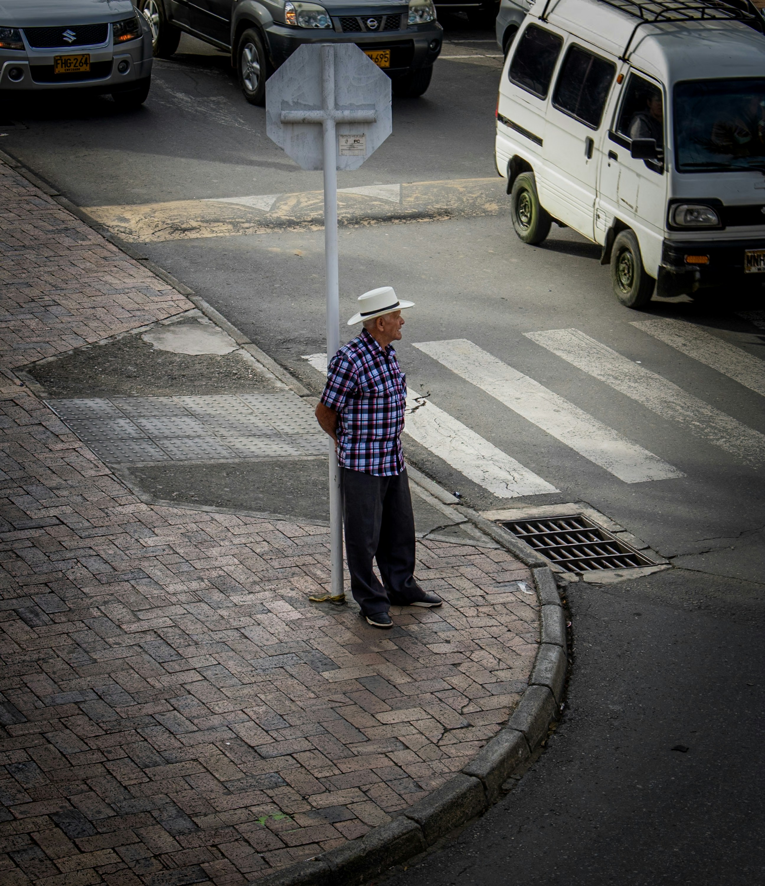 Man in hat waits at a crosswalk with traffic