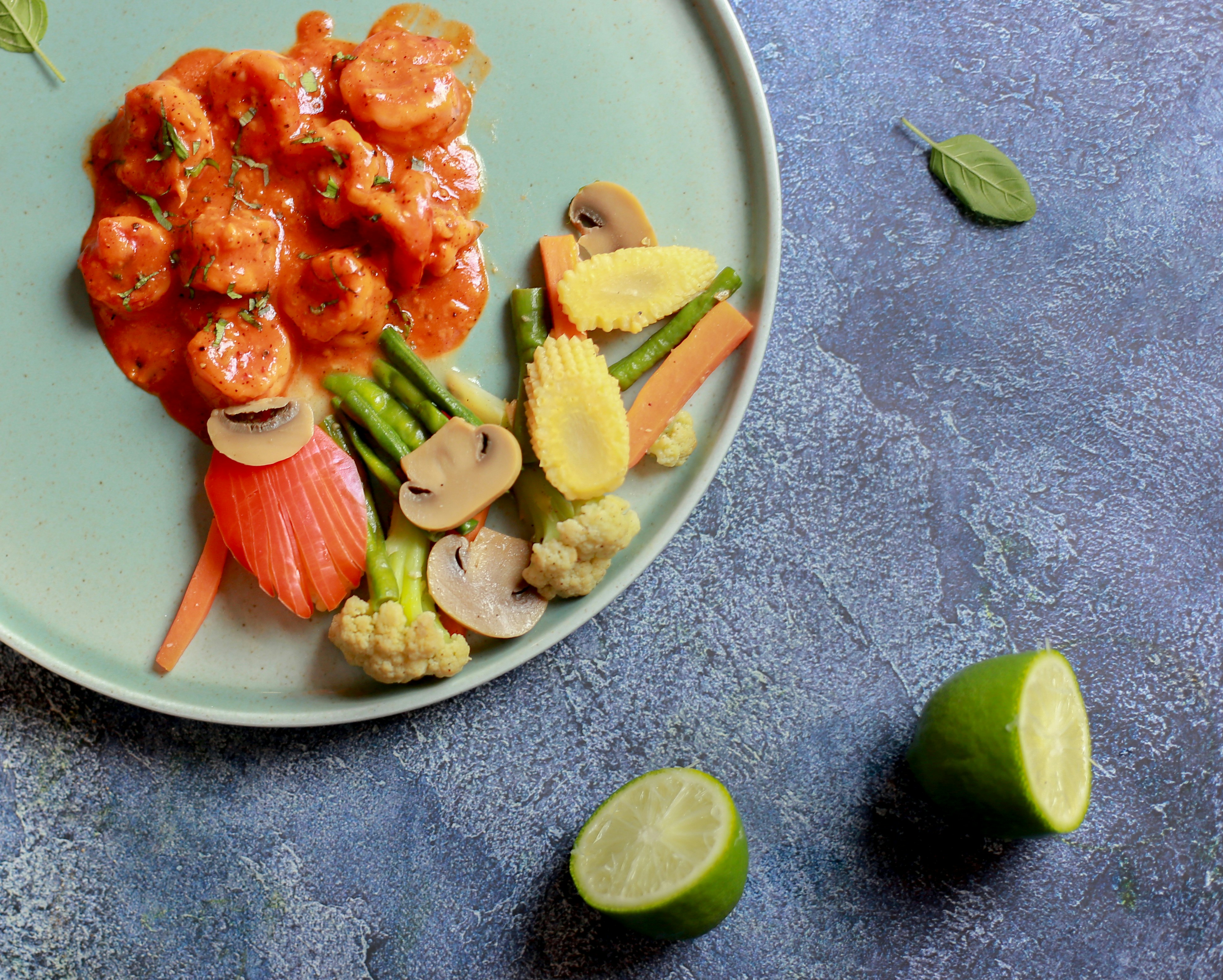 A vibrant plate featuring succulent shrimp in a rich sauce, accompanied by a variety of fresh vegetables and garnished with lime halves.