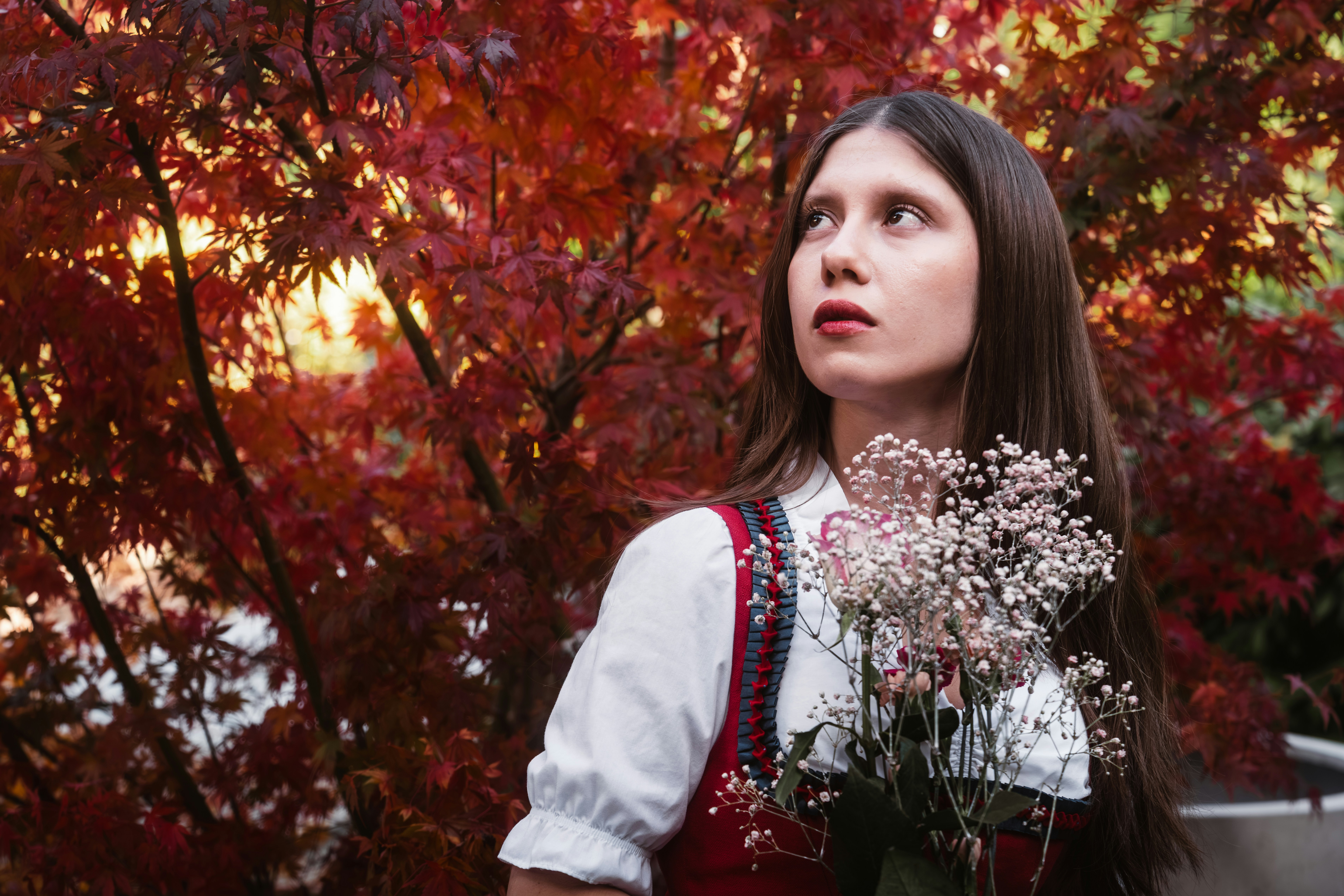 Enchanted moment in fall garden | Woman in traditional dress holding flowers near red leaves