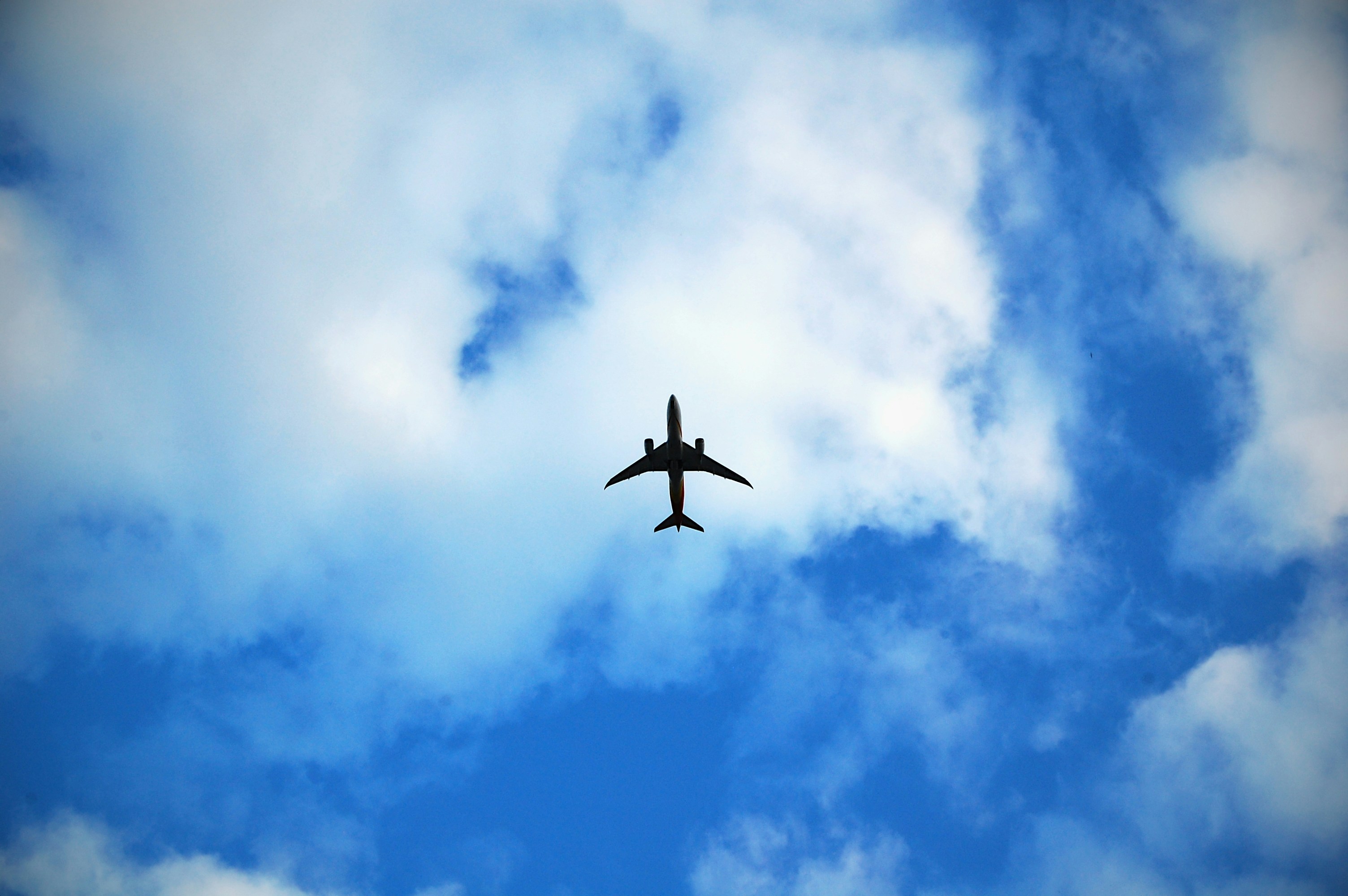 Airplane flying through the sky. | Airplane silhouette against a cloudy blue sky