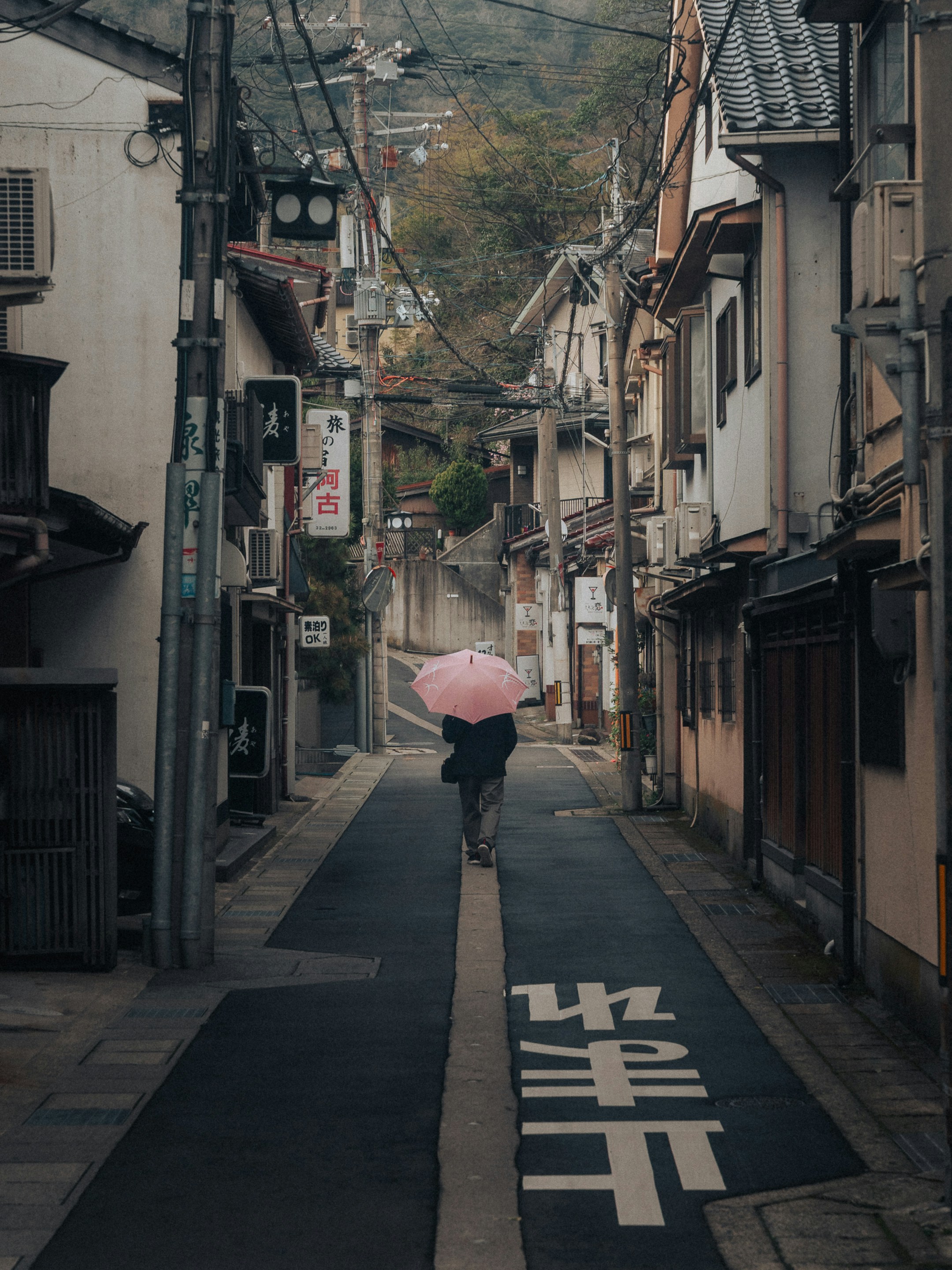 Check out my instagram - @sebastiandugudae | Person with pink umbrella walks down narrow street.