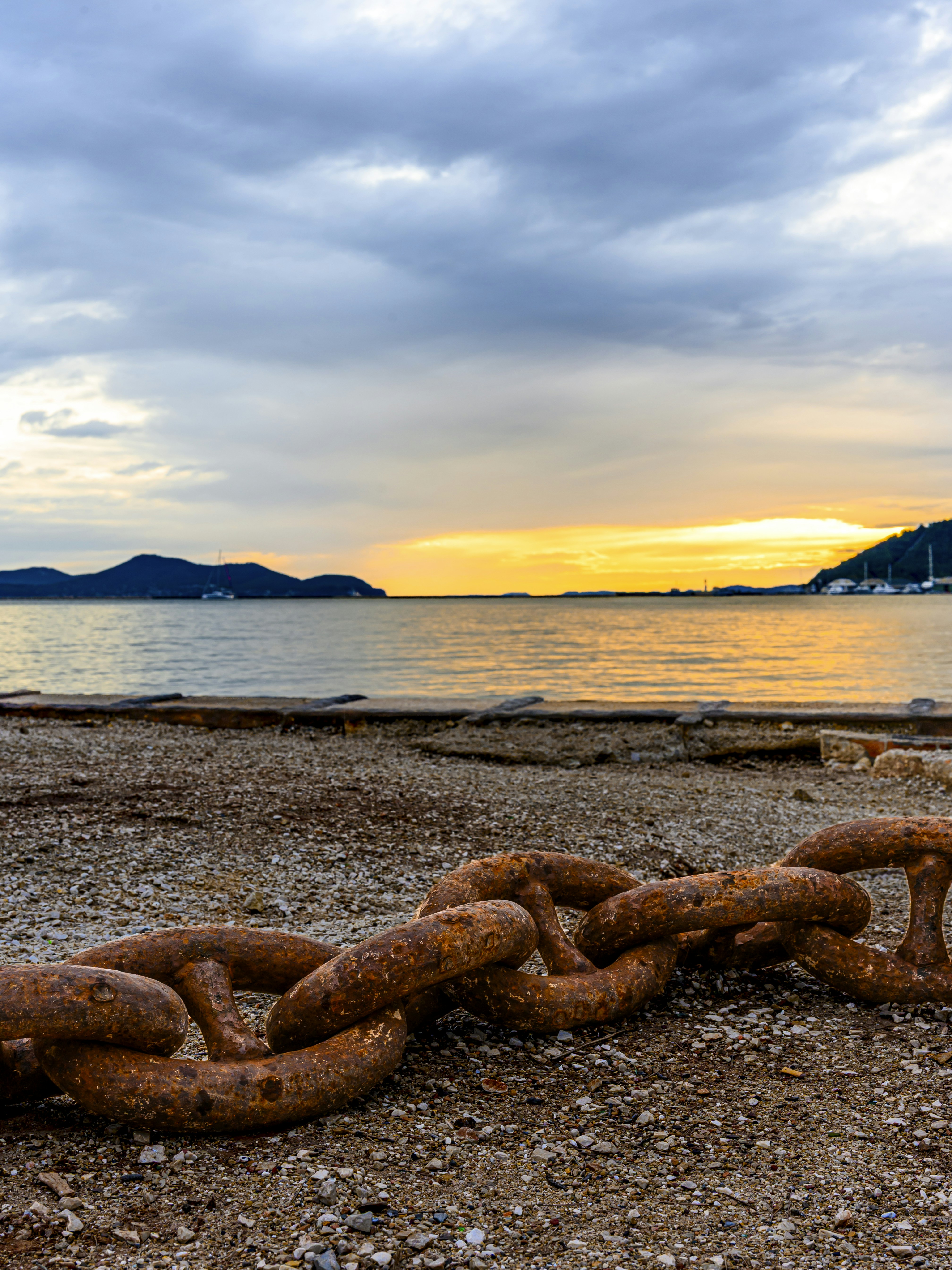 Rusted Links Framing a Sunset Seascape on a Pebble Beach