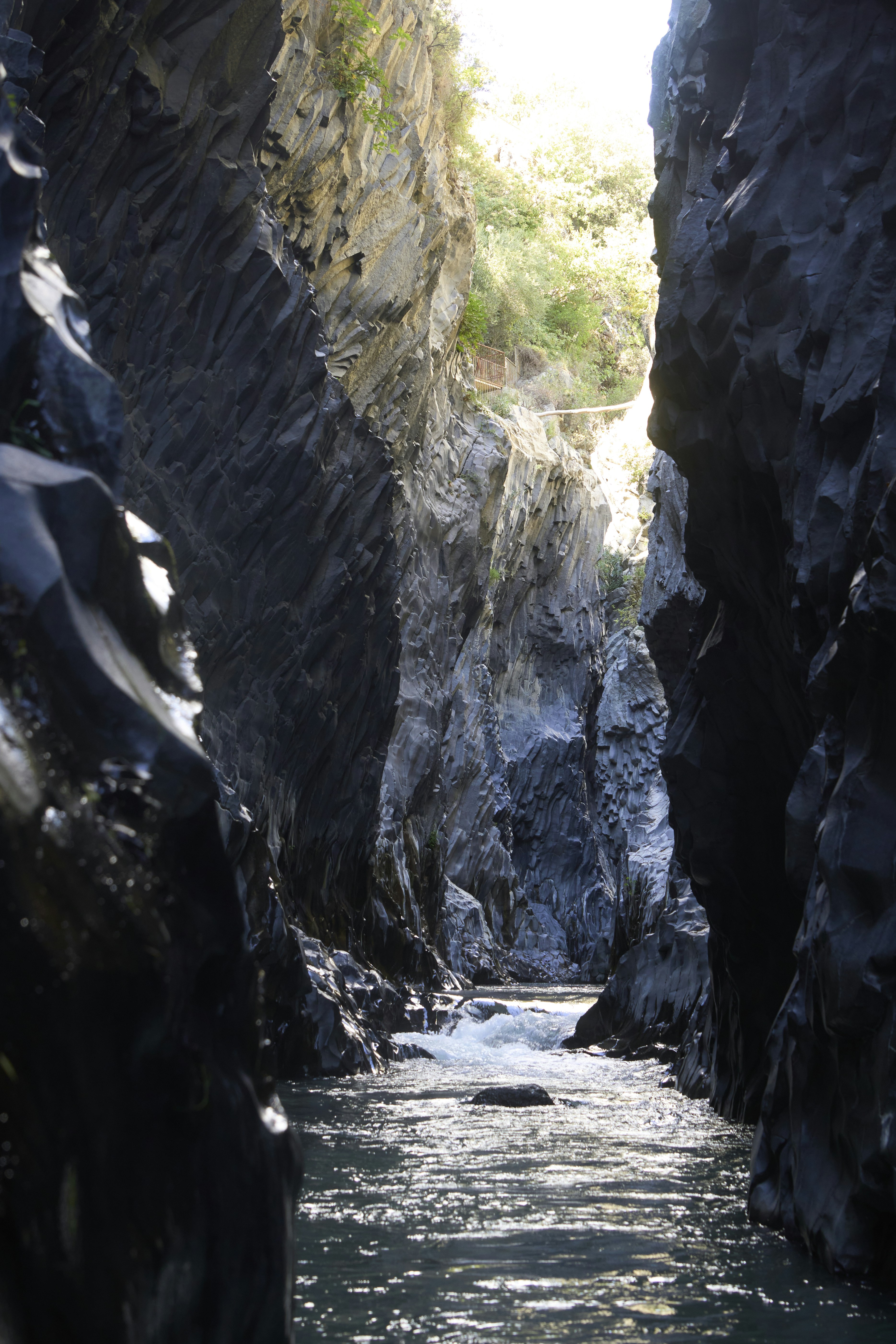 Narrow canyon walls rise steeply above a shimmering river, showcasing the intricate textures of rock and the interplay of light and shadow.