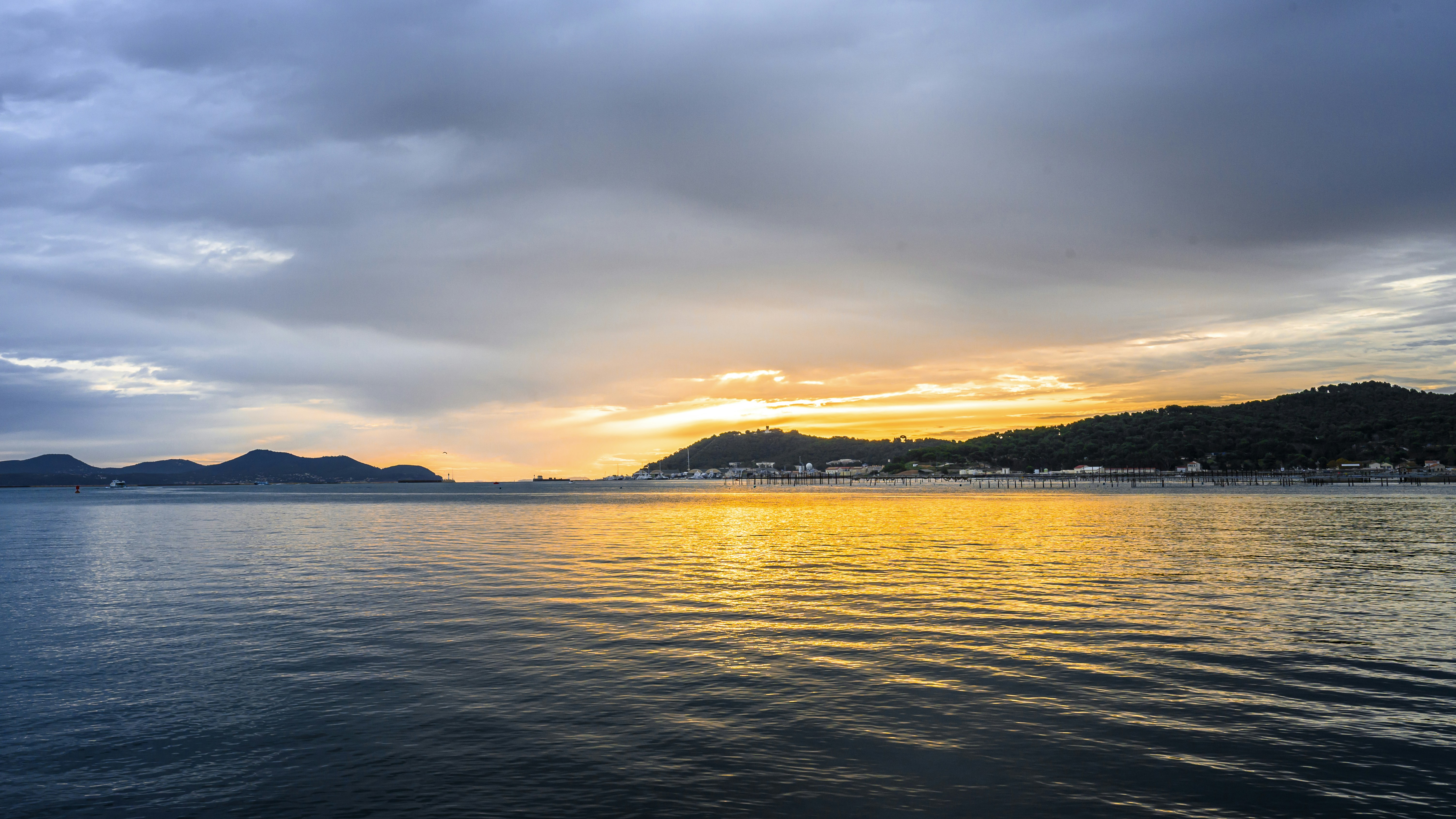 Sunset over a calm ocean with distant hills