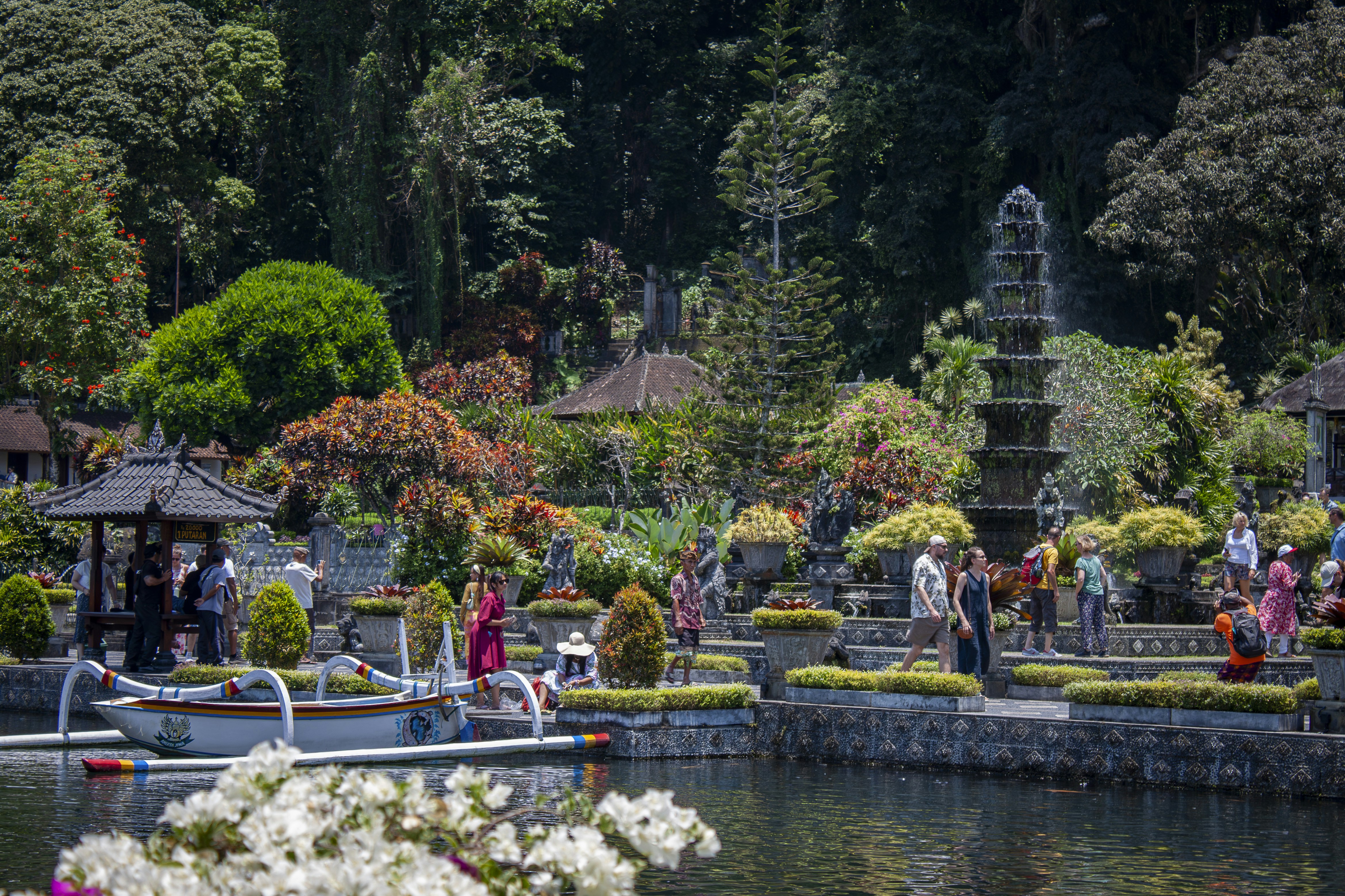 People explore a lush garden with a pond and boat.