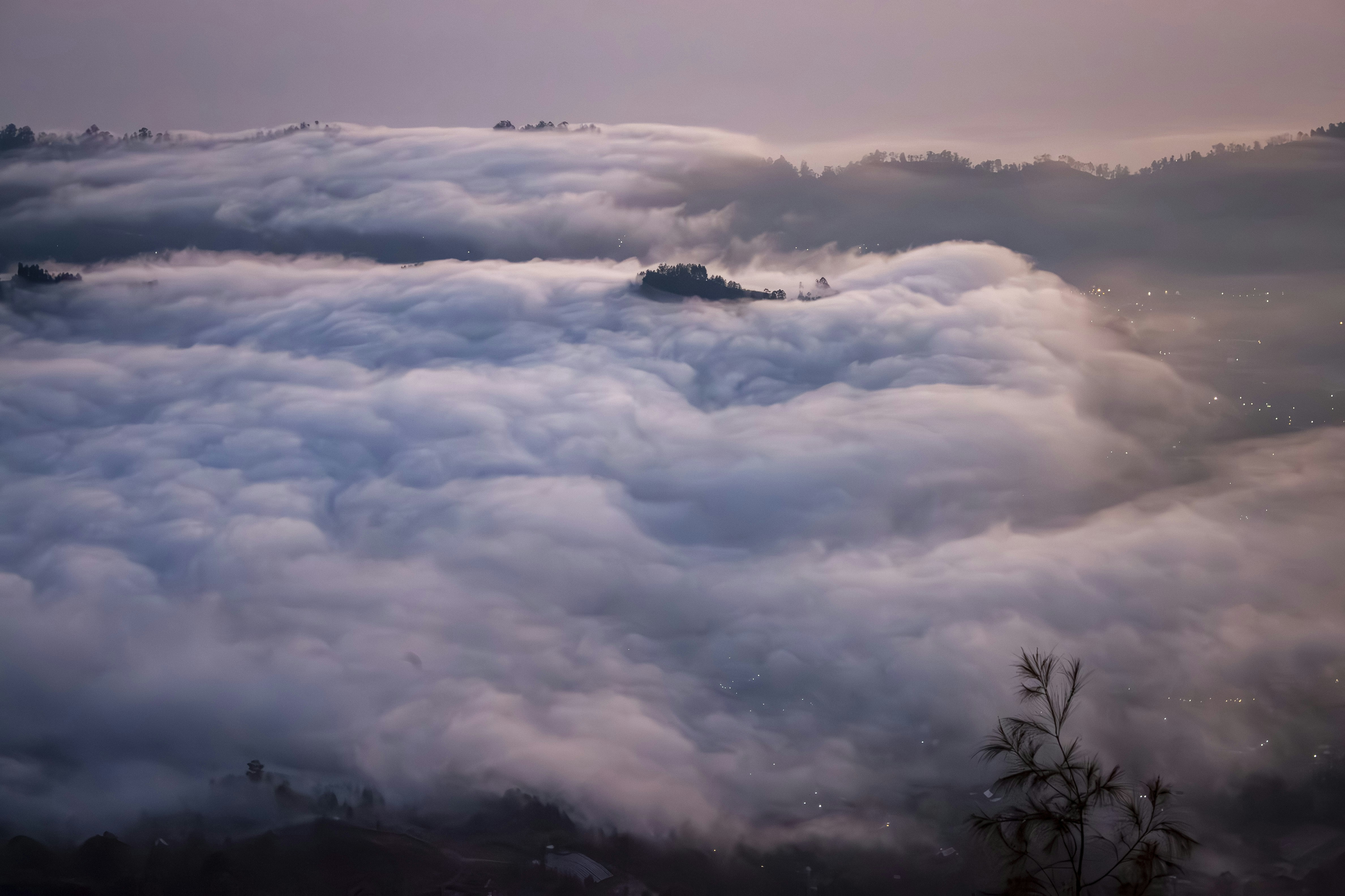 Rolling fog enveloping a valley at twilight, revealing distant lights twinkling through the haze.
