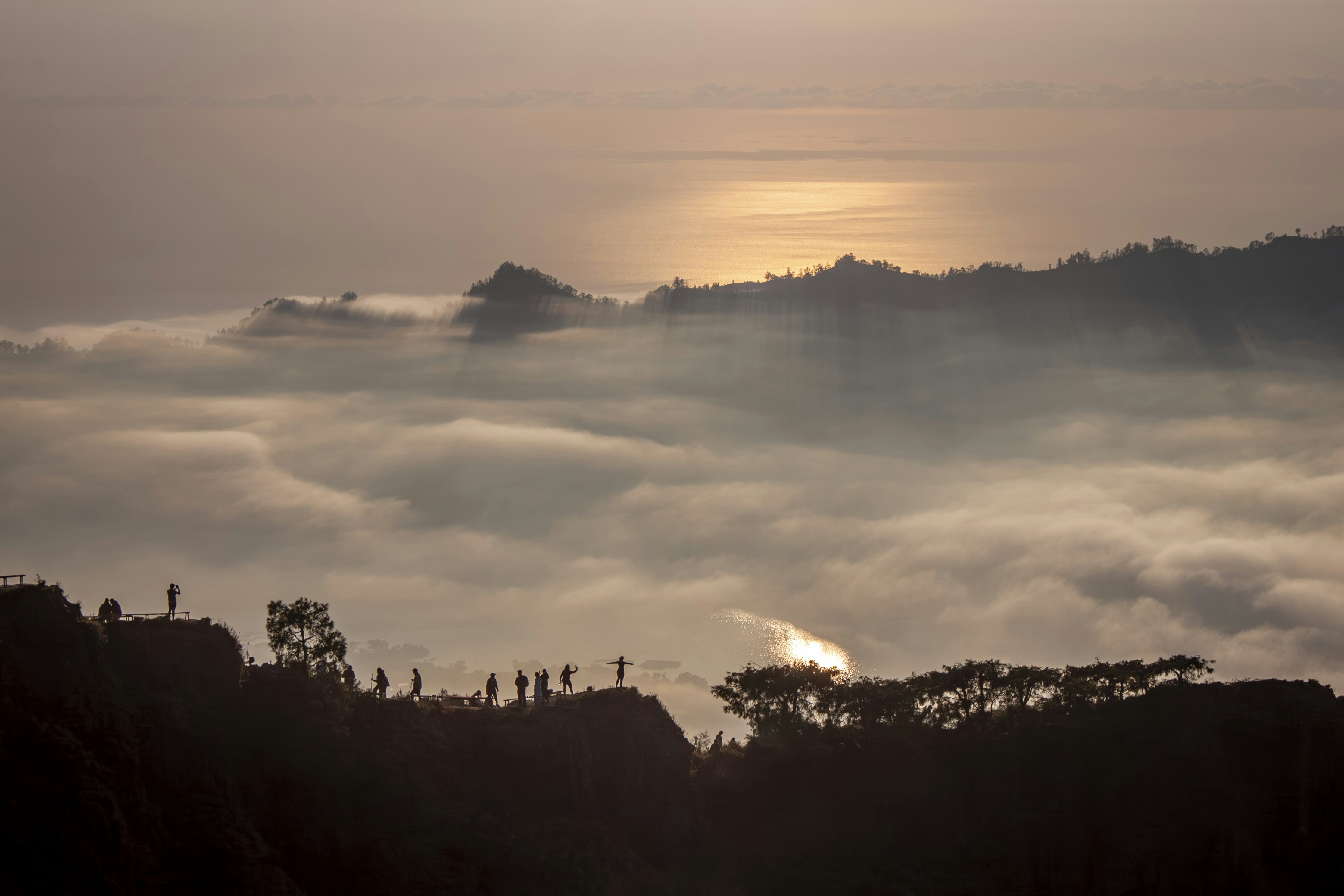 Silhouetted hikers on a ridge overlooking misty mountains at sunrise