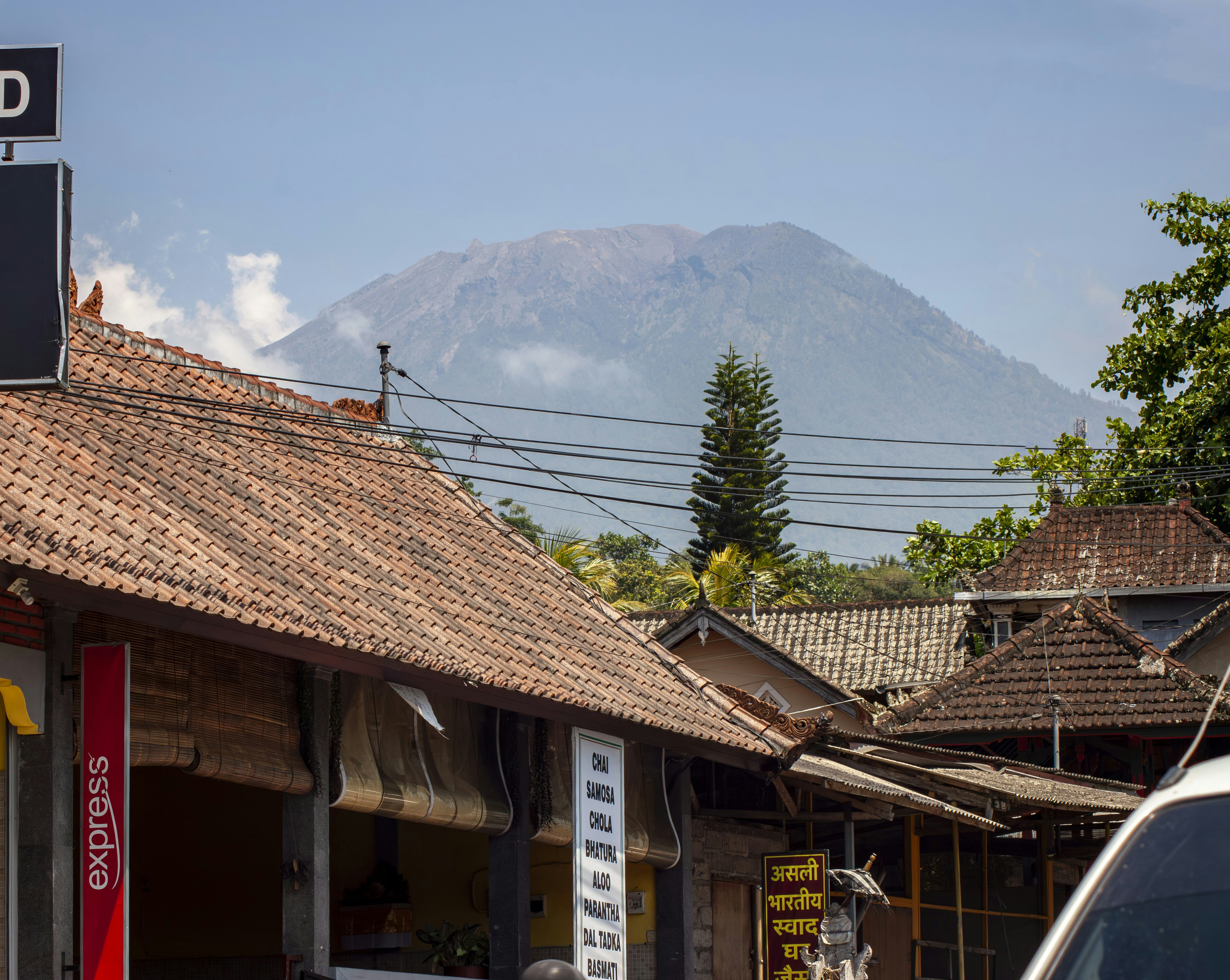 Volcano looms over village rooftops under a clear sky.
