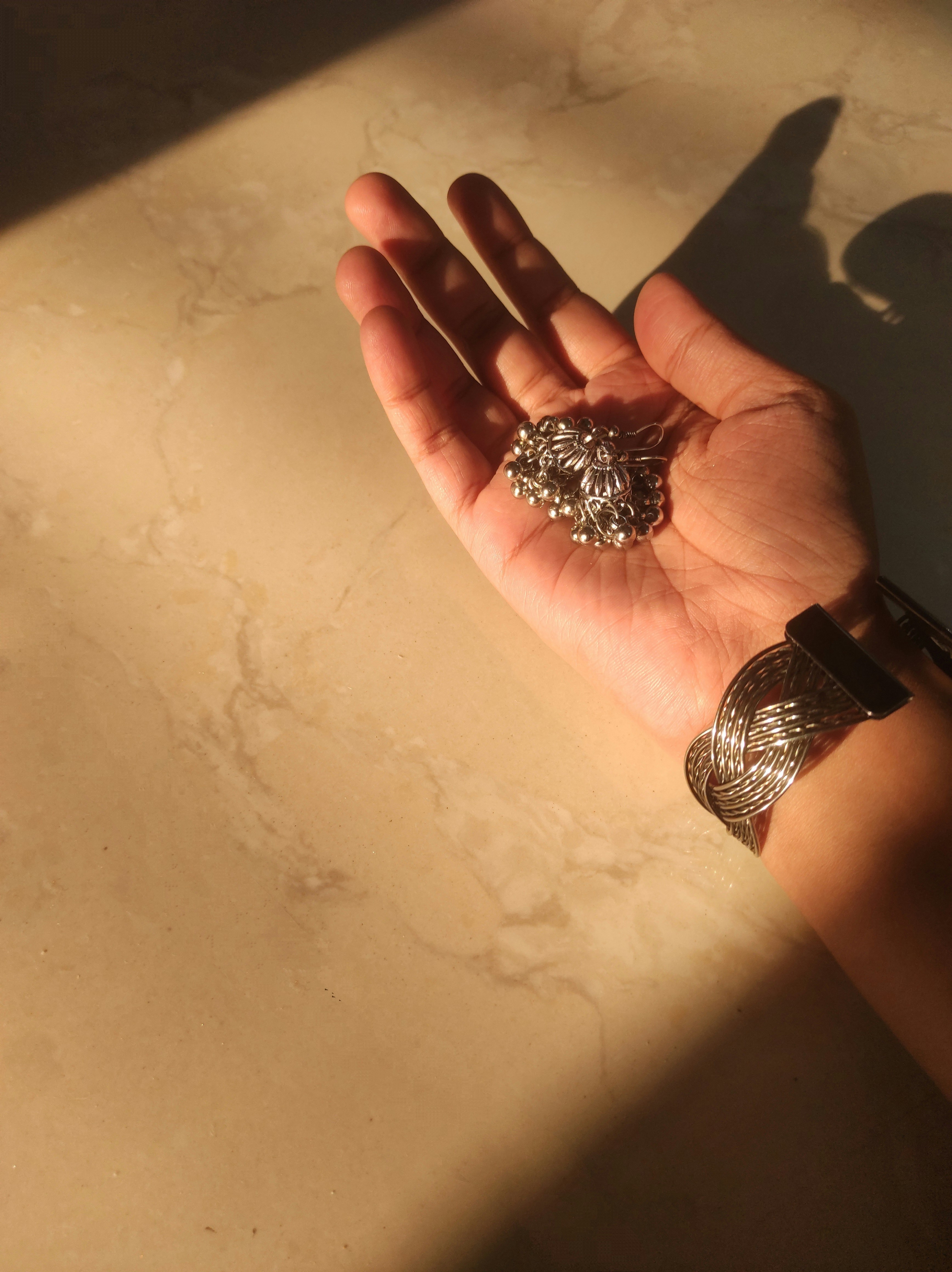 Hand holding silver brooch with braided bracelet.