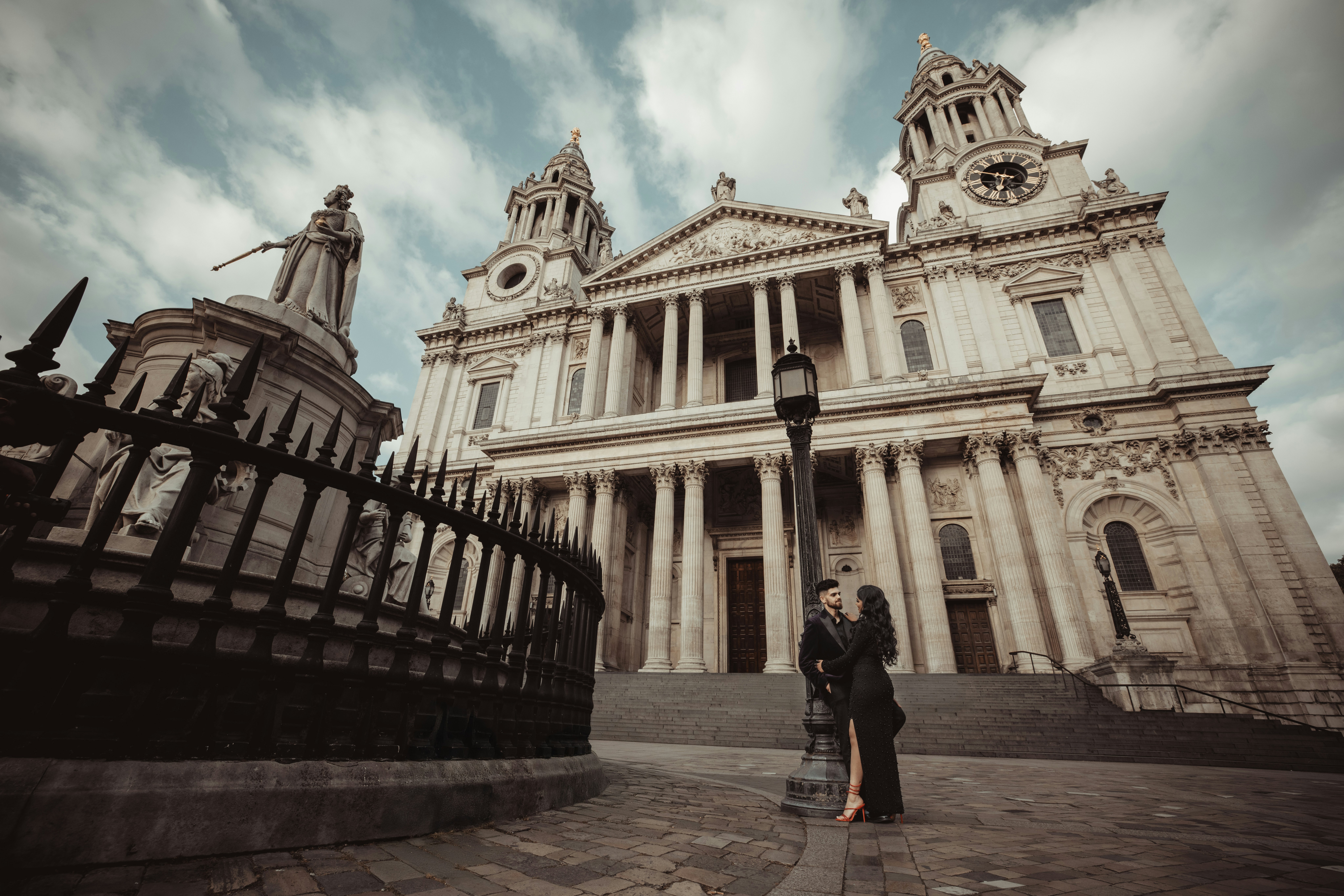 Couple embracing near the iconic St. Paul's Cathedral, framed by ornate architecture and dramatic skies.