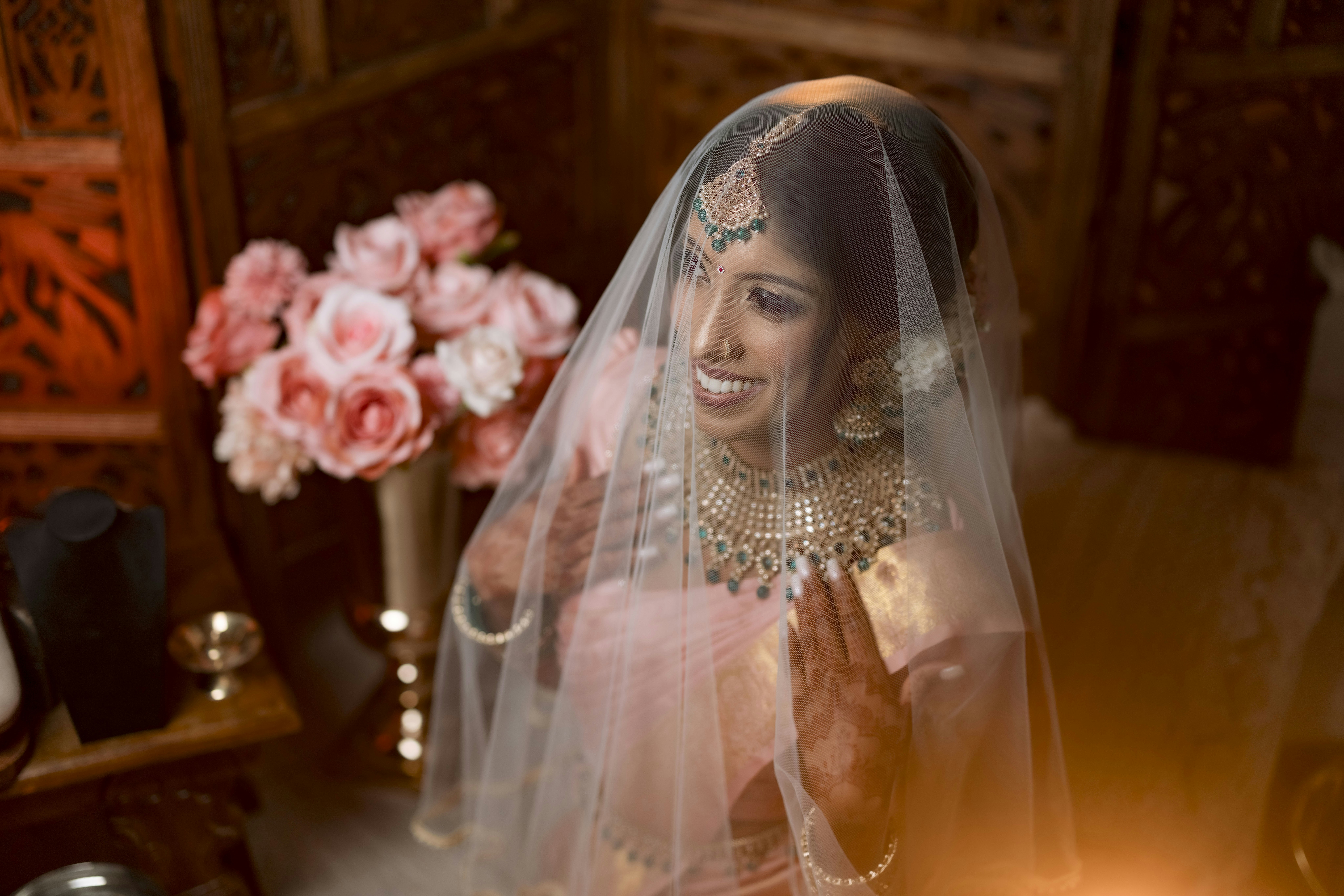 A bride in a pink dress and veil smiles.
