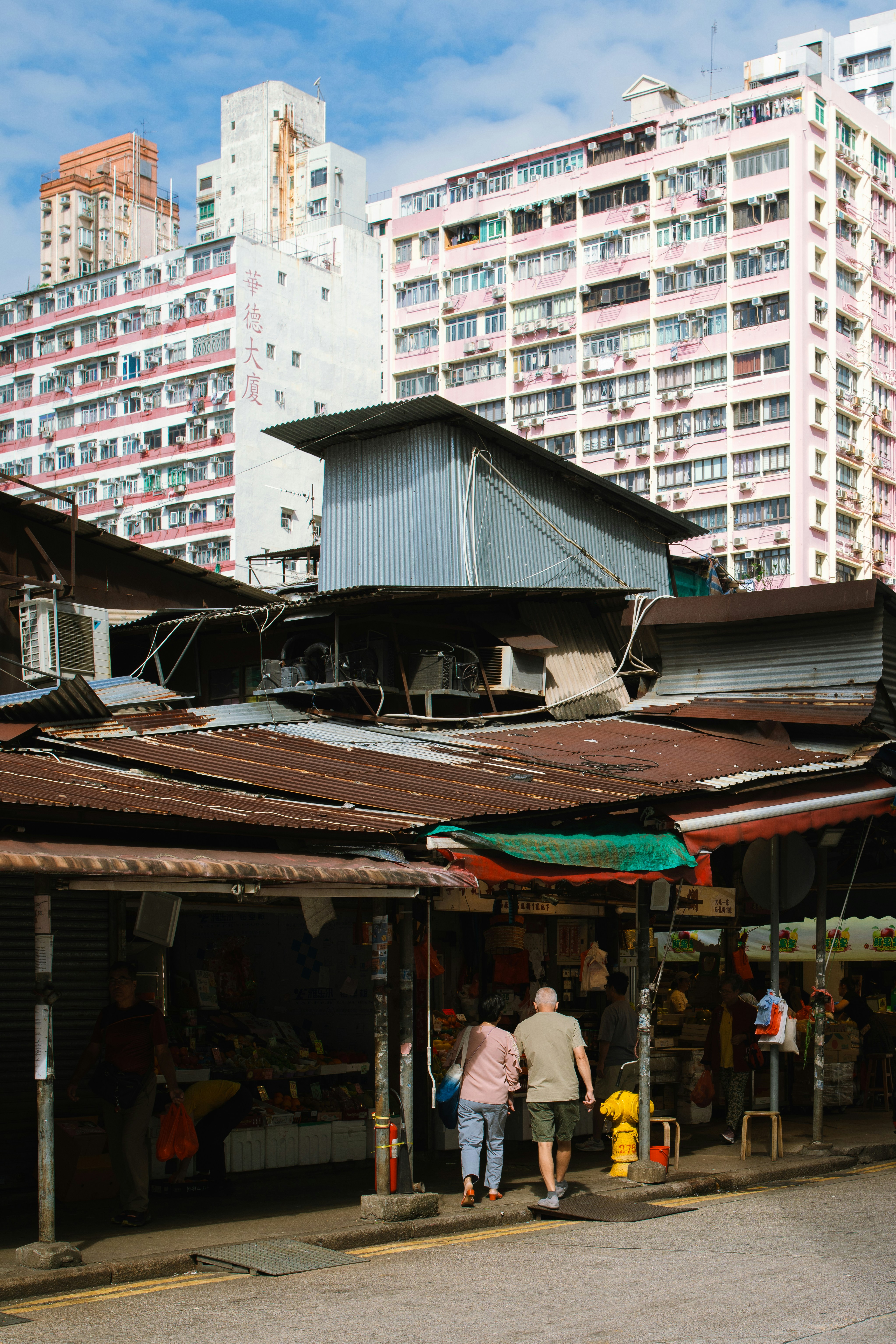 People walk past market stalls with apartment buildings behind.