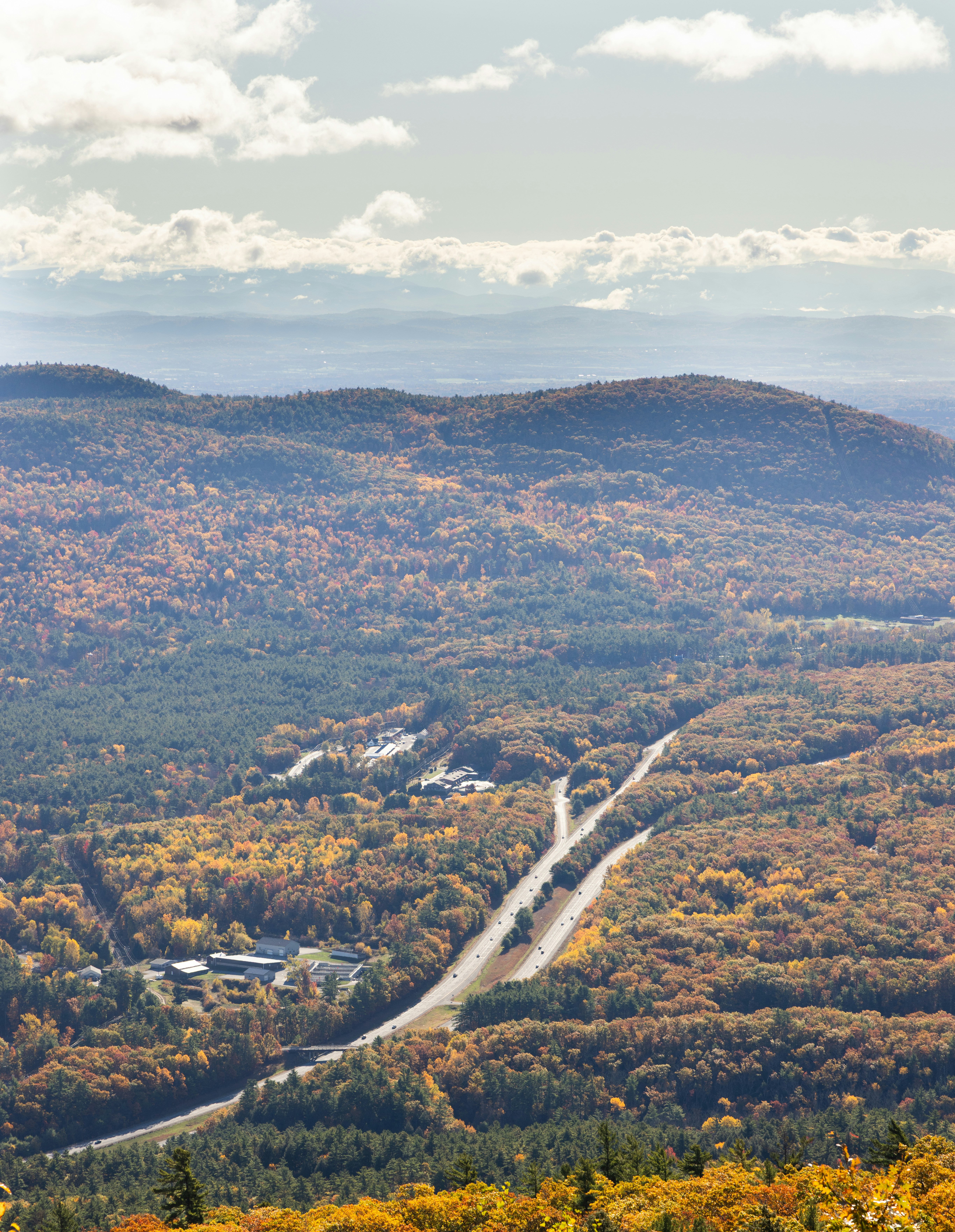 Vibrant autumn foliage blankets the hills, with a winding road cutting through the landscape. The scene captures the essence of seasonal transition.