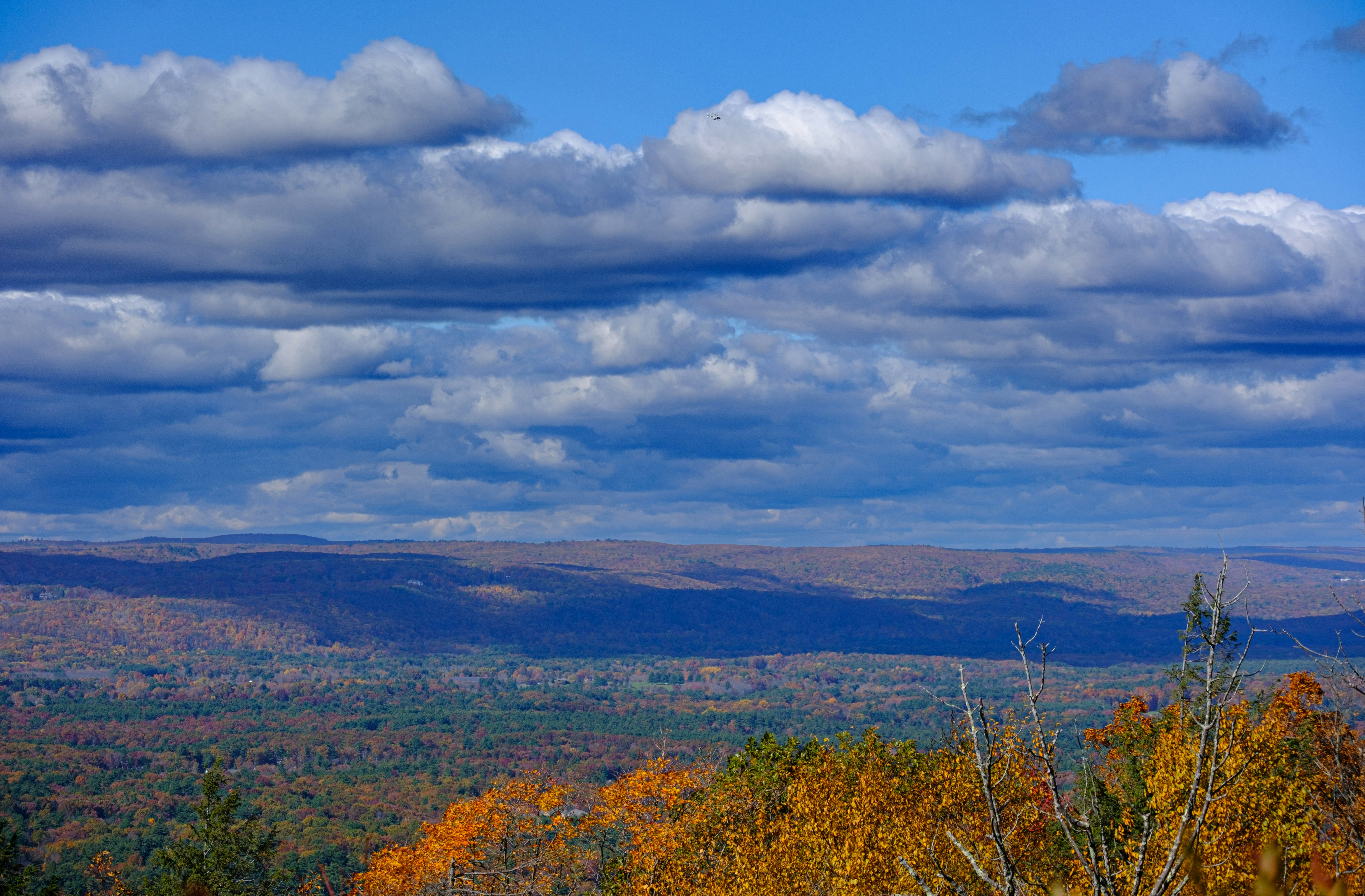 Vibrant autumn foliage blankets the hills beneath a dynamic sky filled with fluffy clouds. The scene conveys the tranquil beauty of nature in transition.