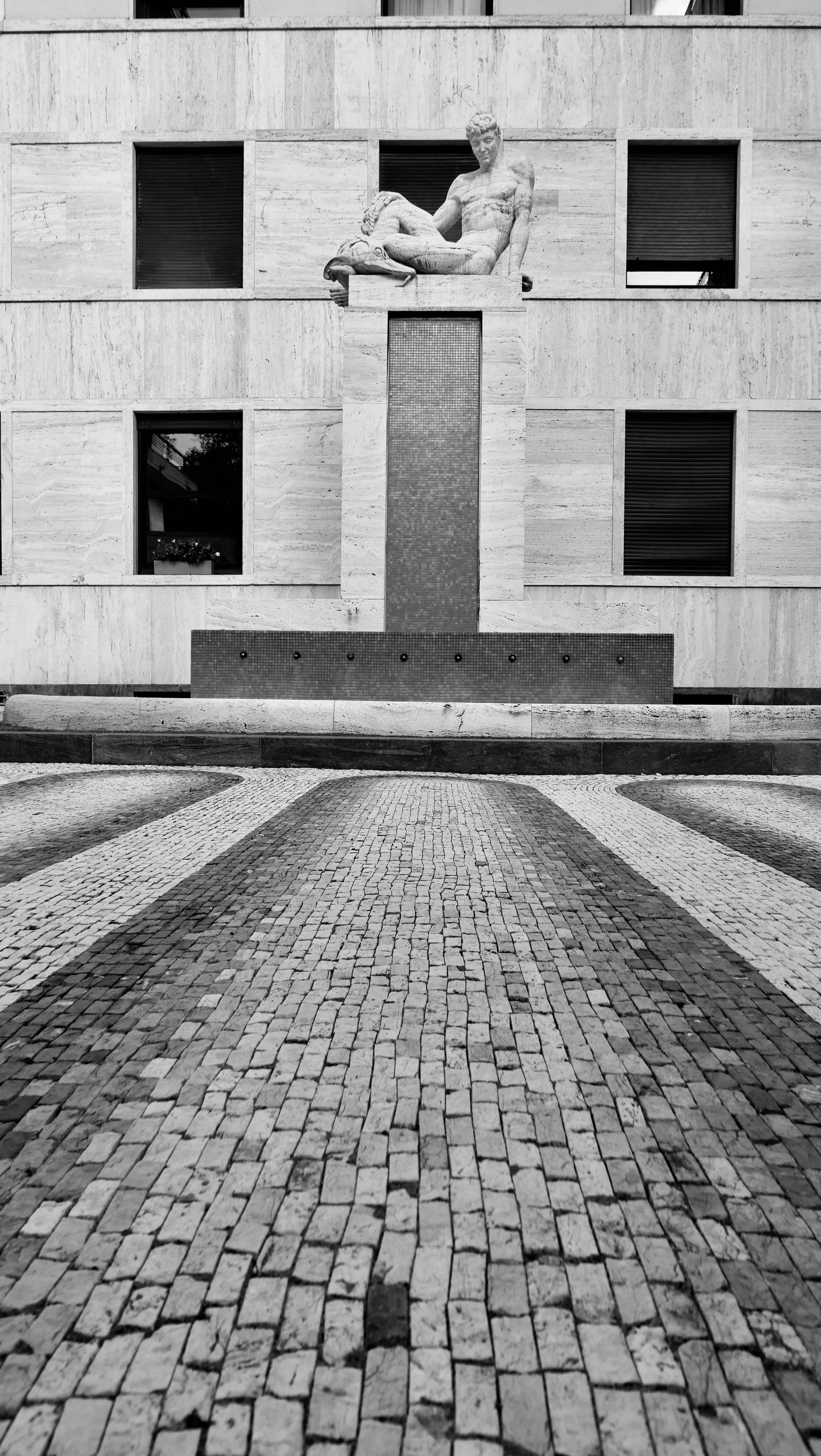Casa della Fontana | Sculpture on a marble building facade with patterned pavement