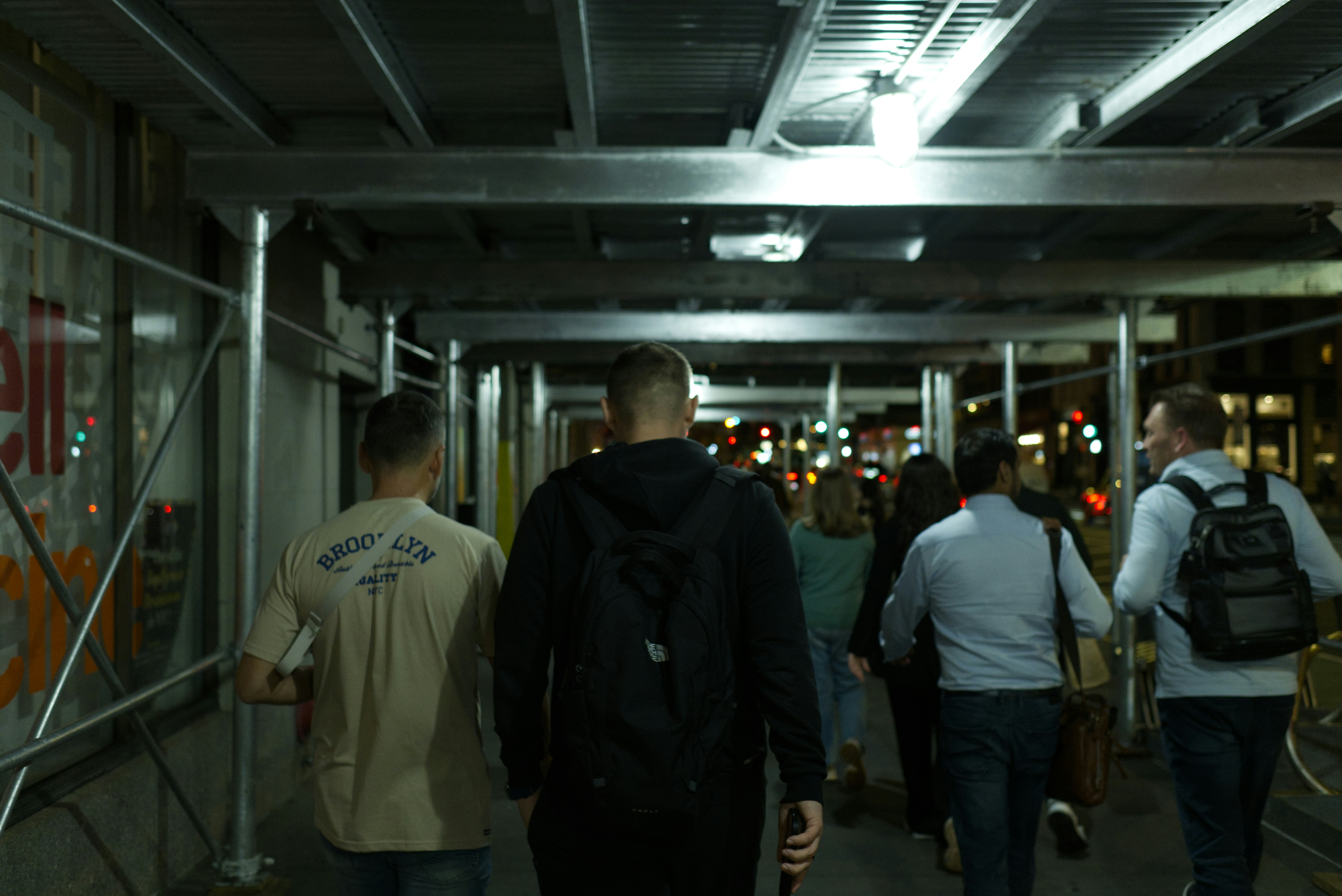 A group of pedestrians walking under a construction scaffold in a bustling urban environment at night.