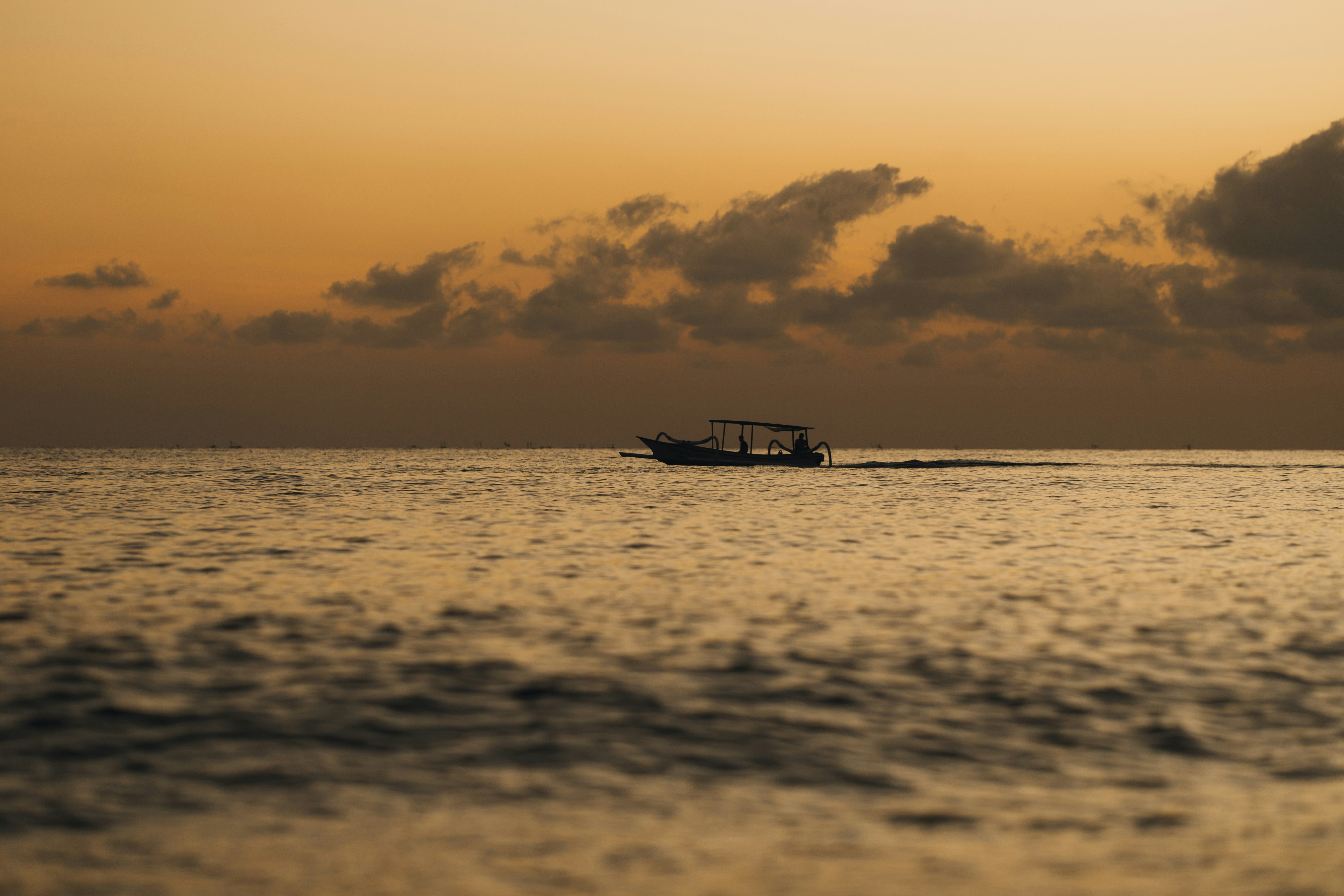 A small boat sails on the ocean at sunset.