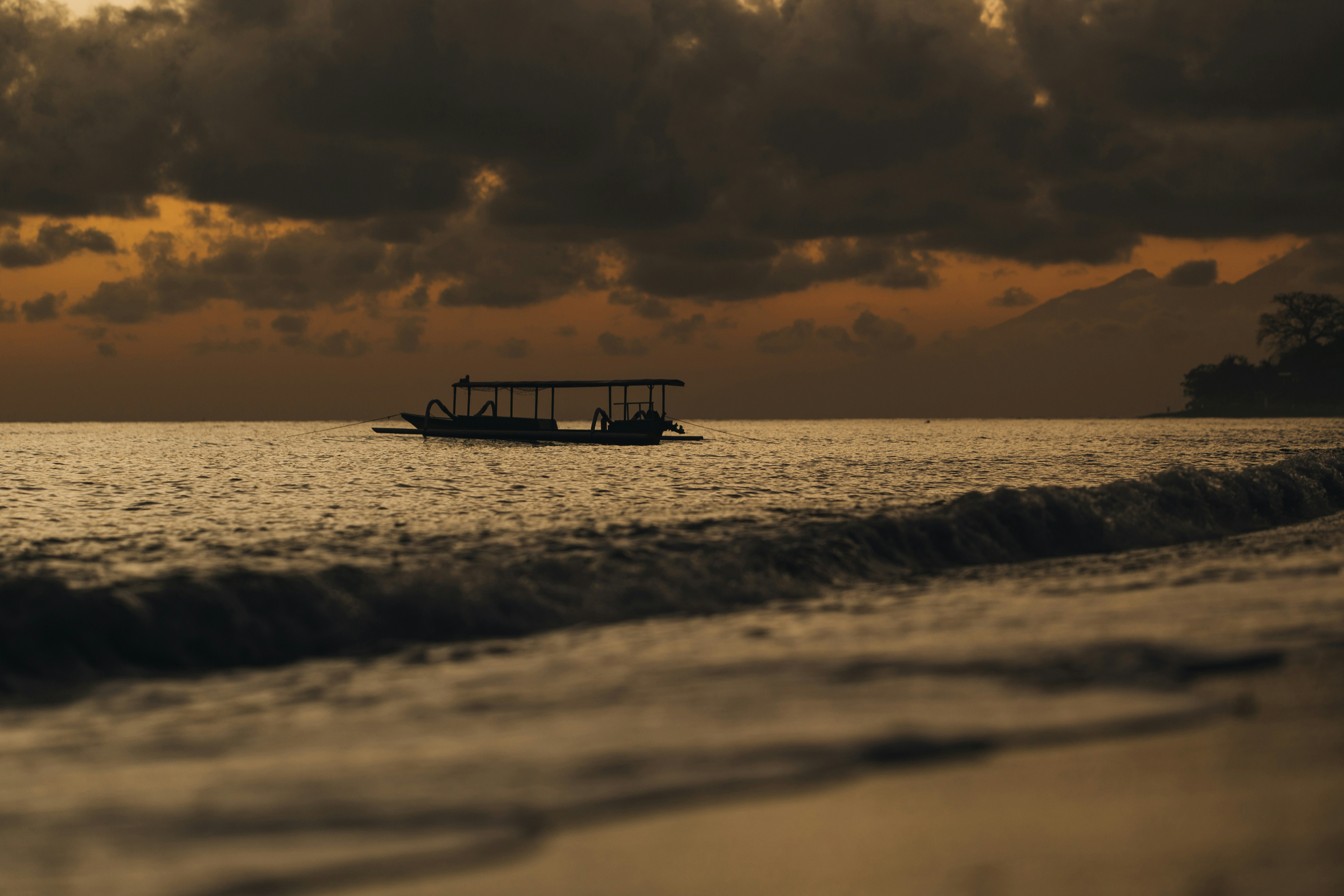 A small boat floats on the ocean at sunset.