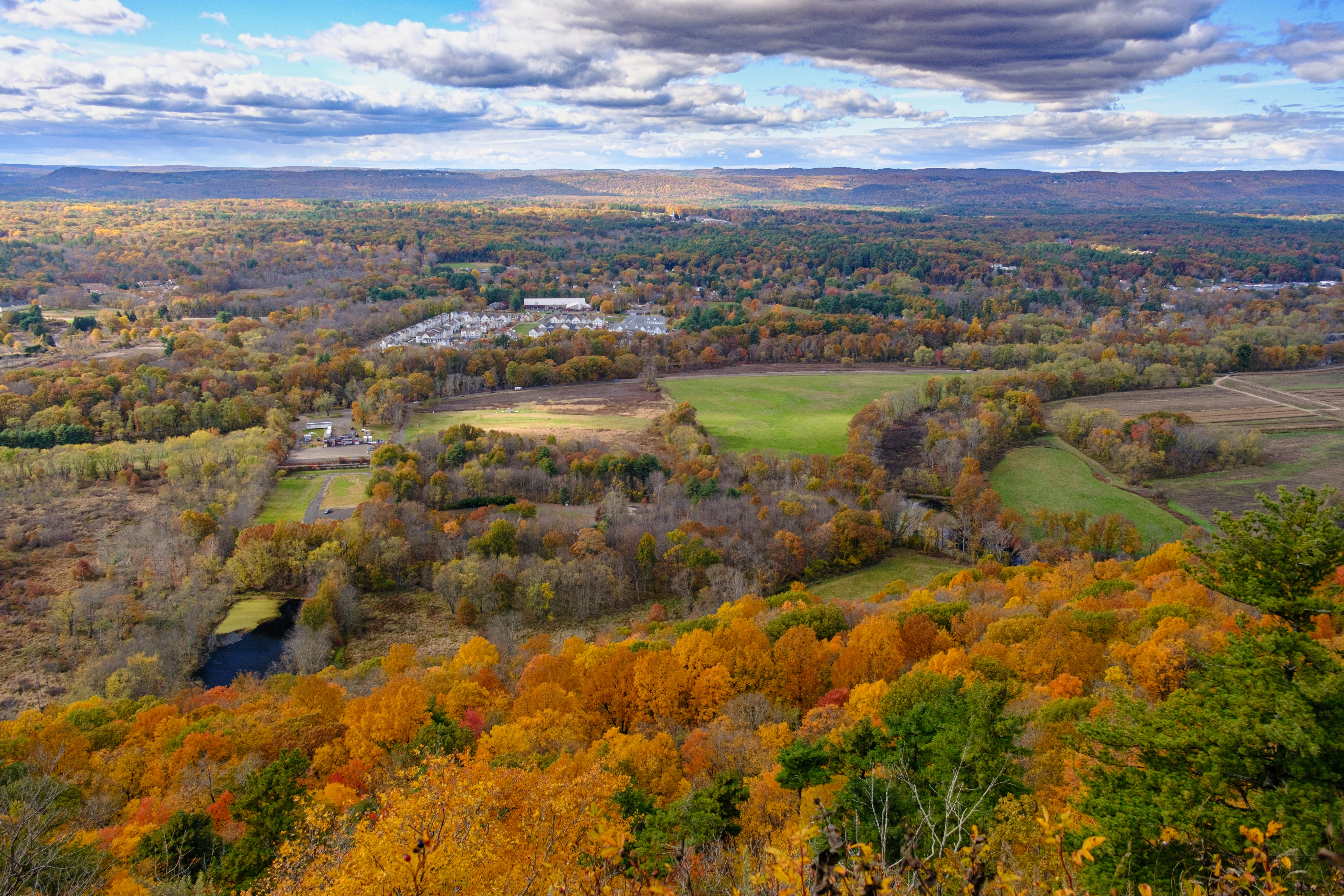 Vibrant autumn foliage blankets the landscape, showcasing a mix of orange, yellow, and green hues under a dramatic sky. The view captures the serene beauty of the changing seasons.