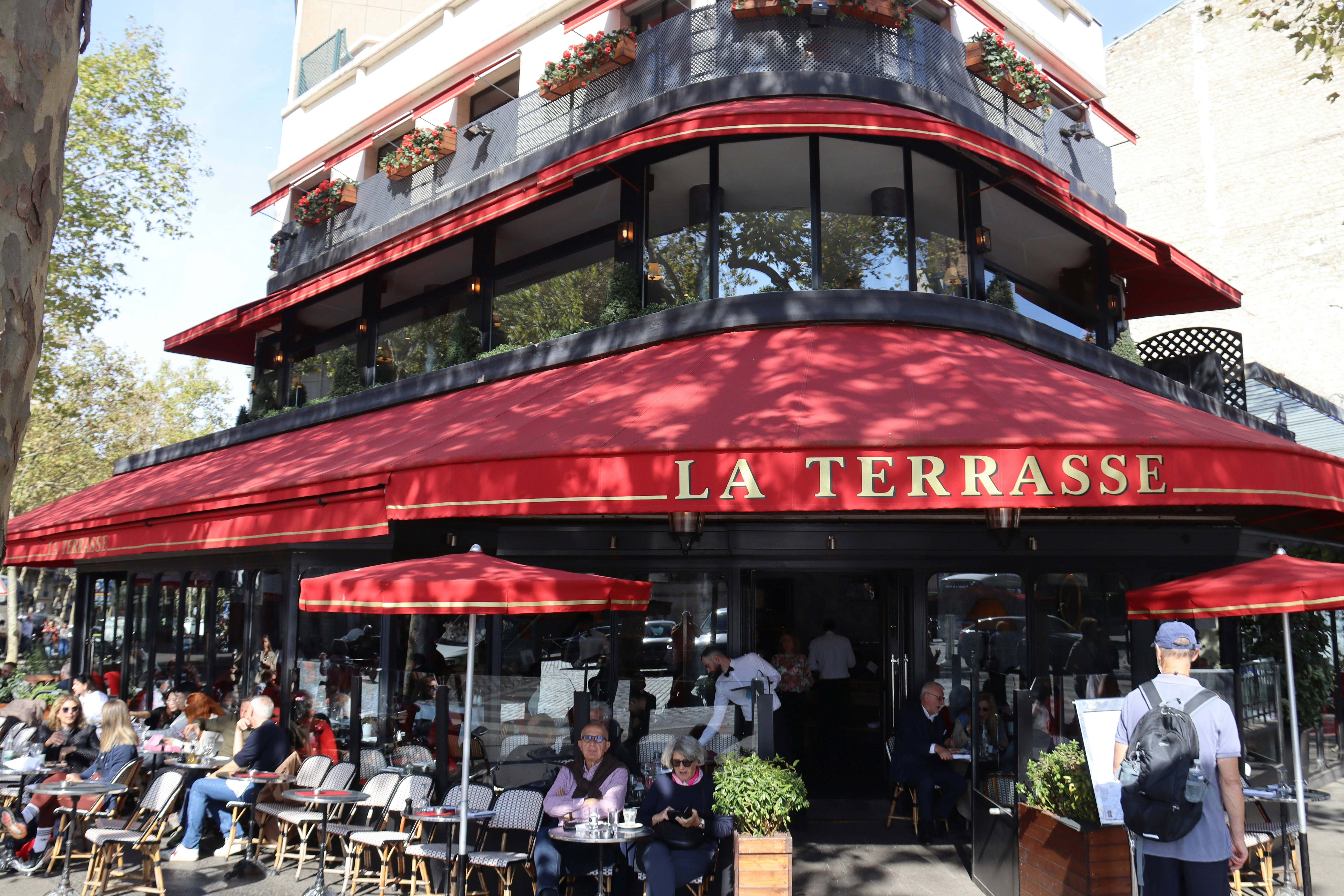 People sit outside a cafe with red awnings.