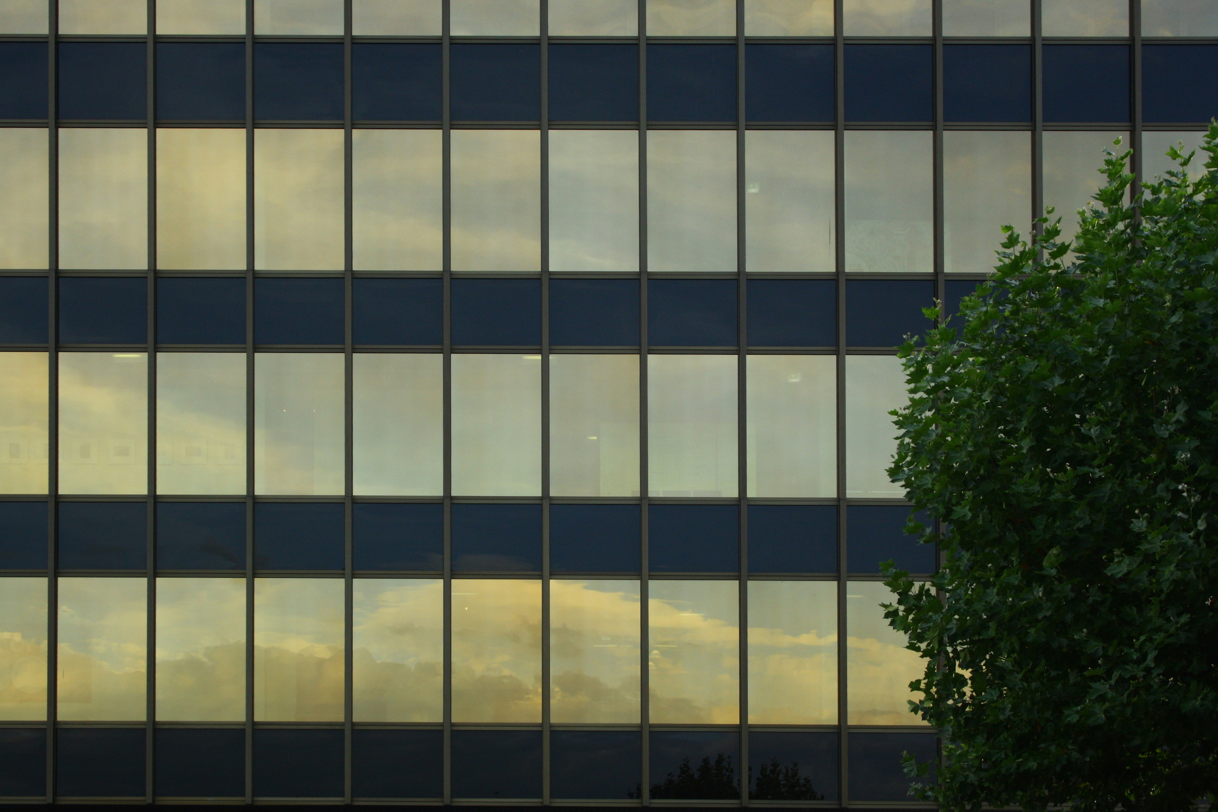 Modern building facade with reflective windows and cloudy sky.