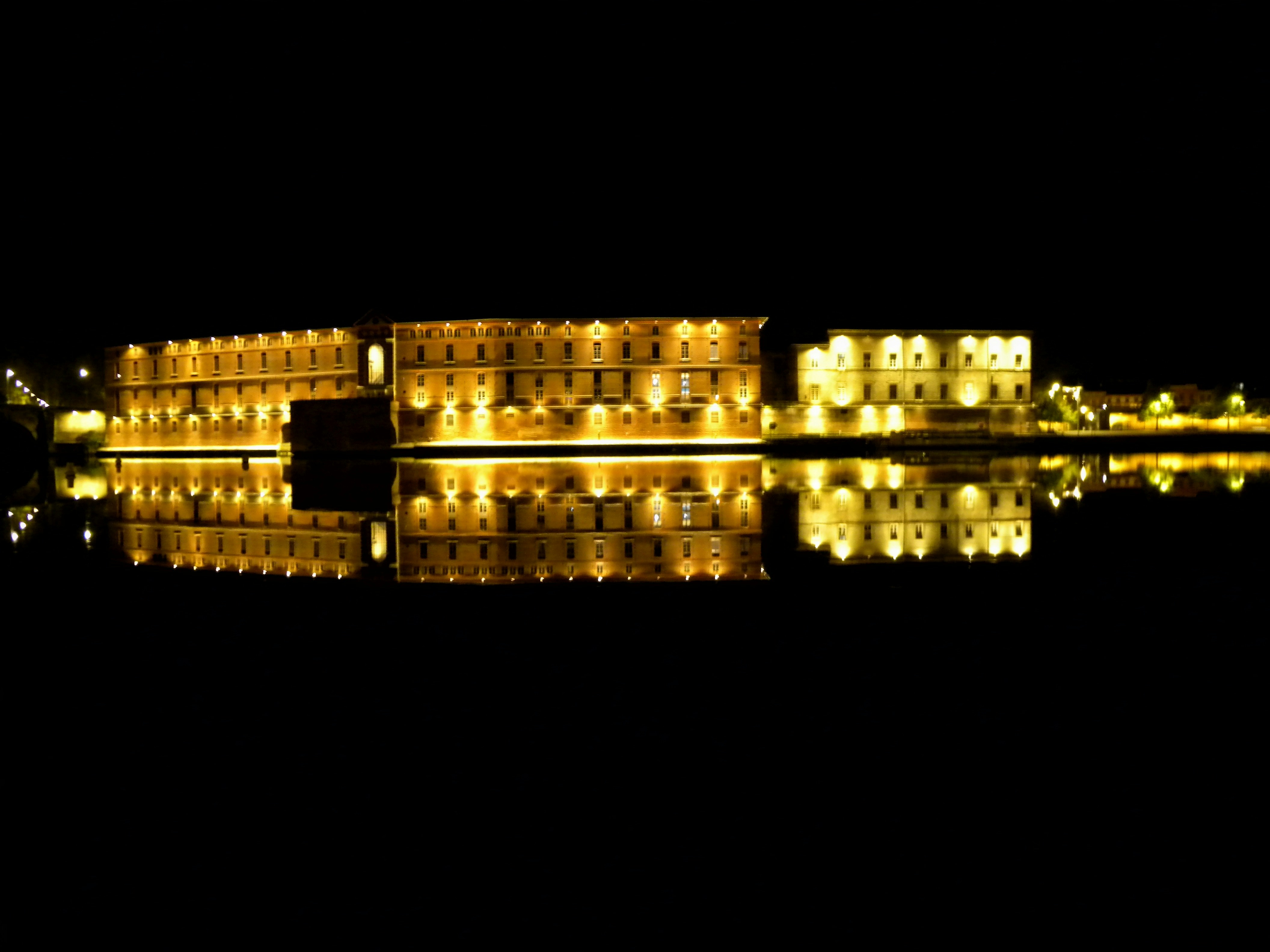 A brightly lit building reflected in dark water at night.
