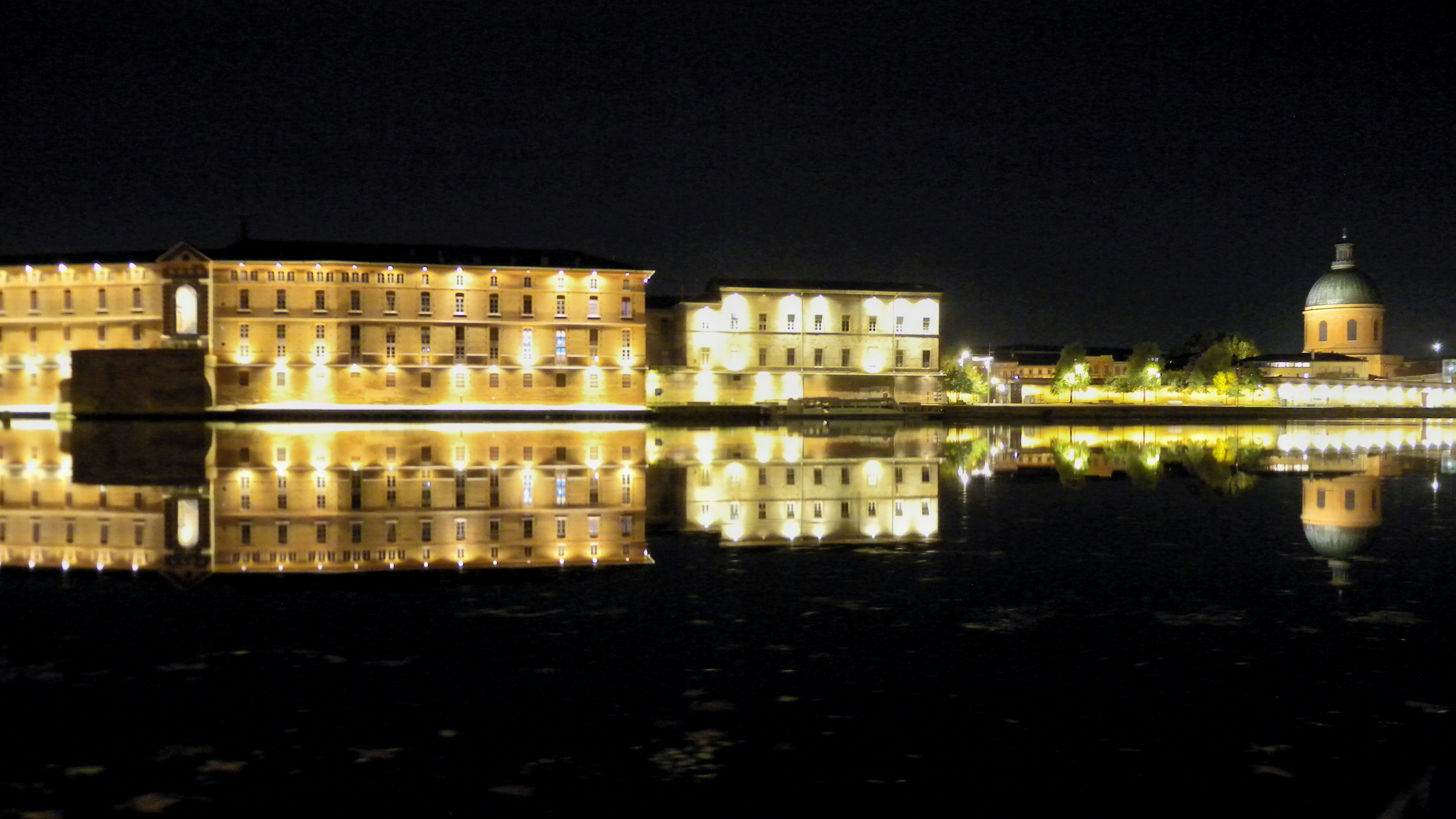 Illuminated buildings reflected in dark water at night.