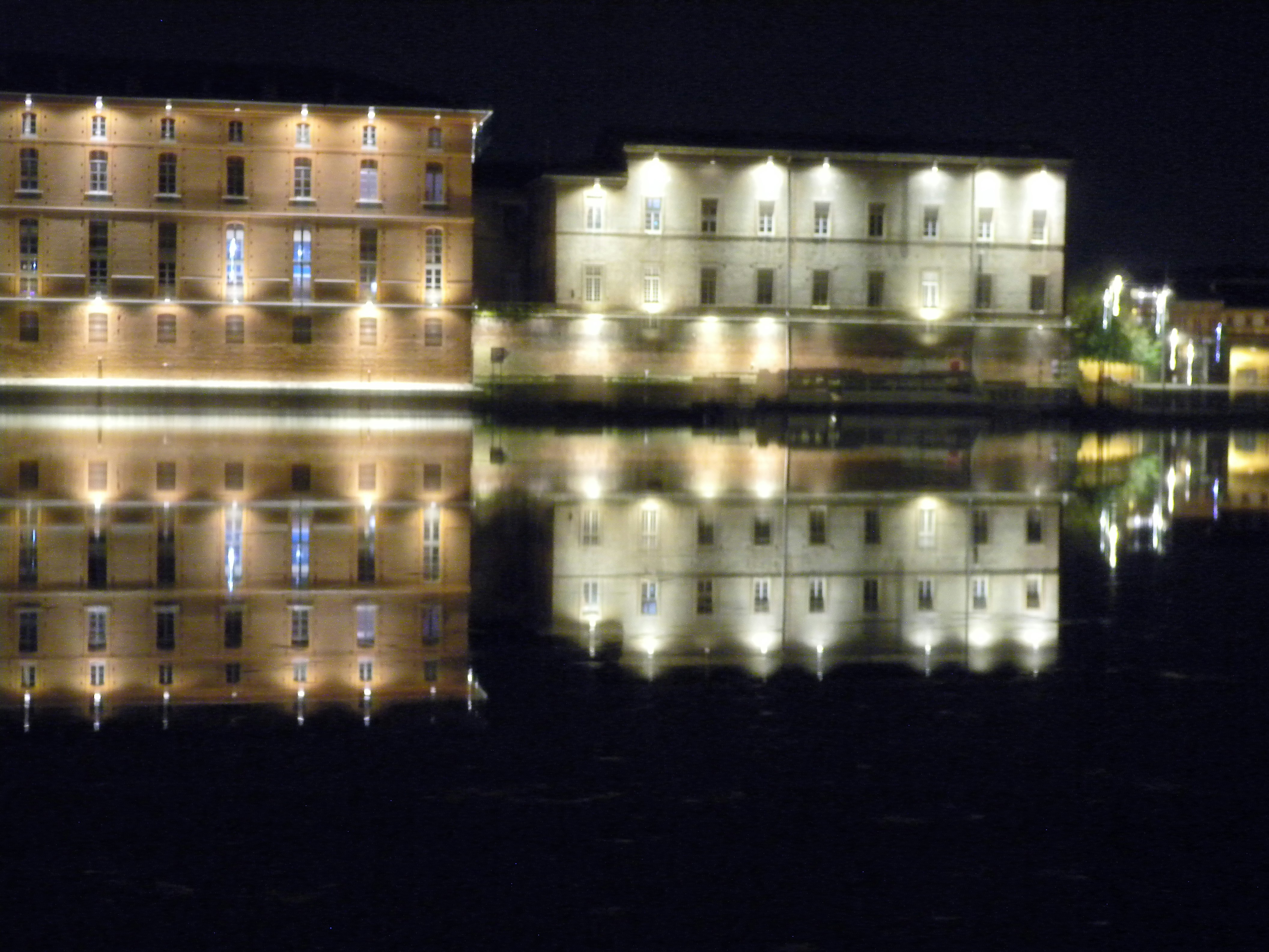 Buildings illuminated at night reflected in water.