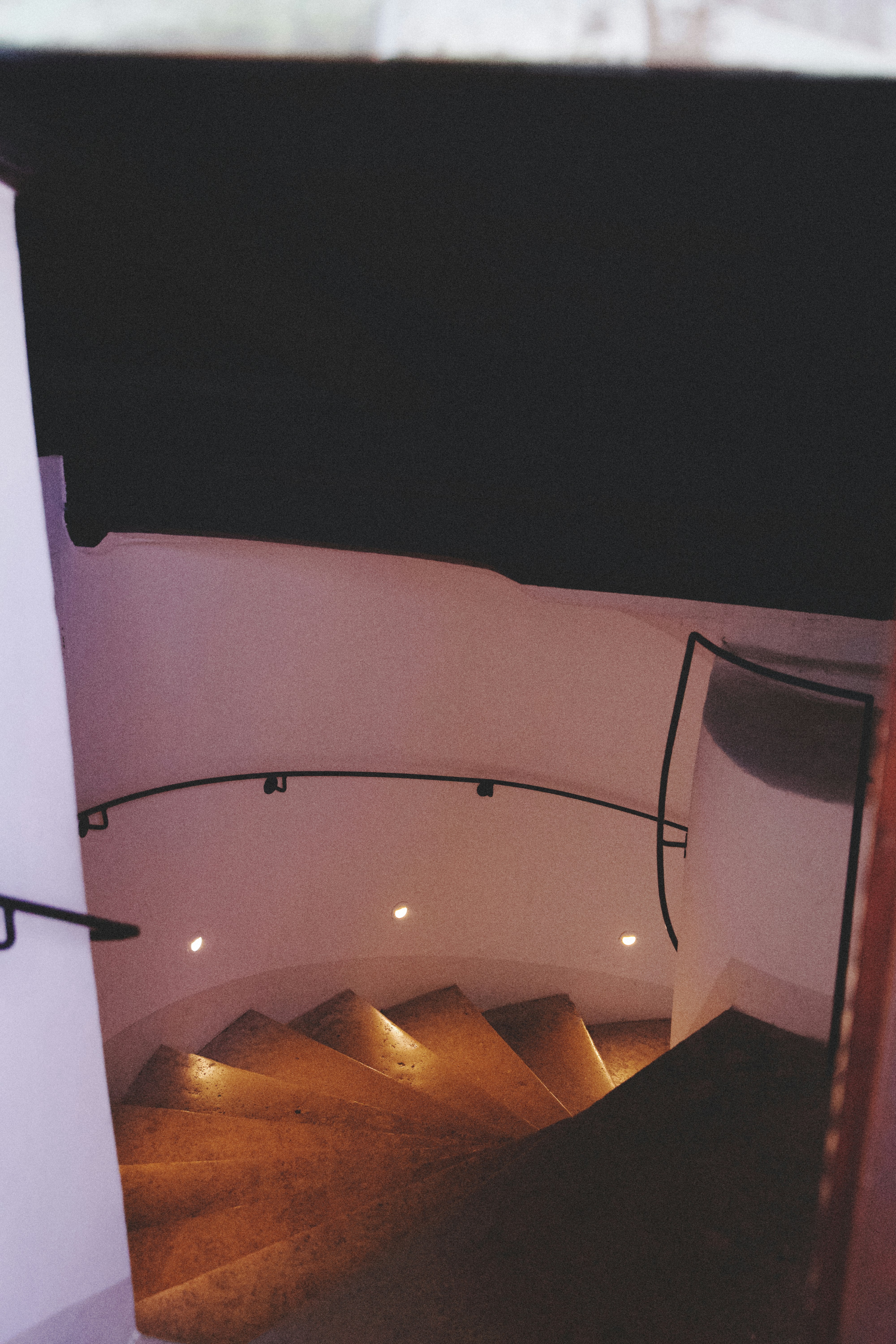 The spiral staircase of the Karlskirche in Vienna. | Spiral staircase with warm lighting descending downwards.