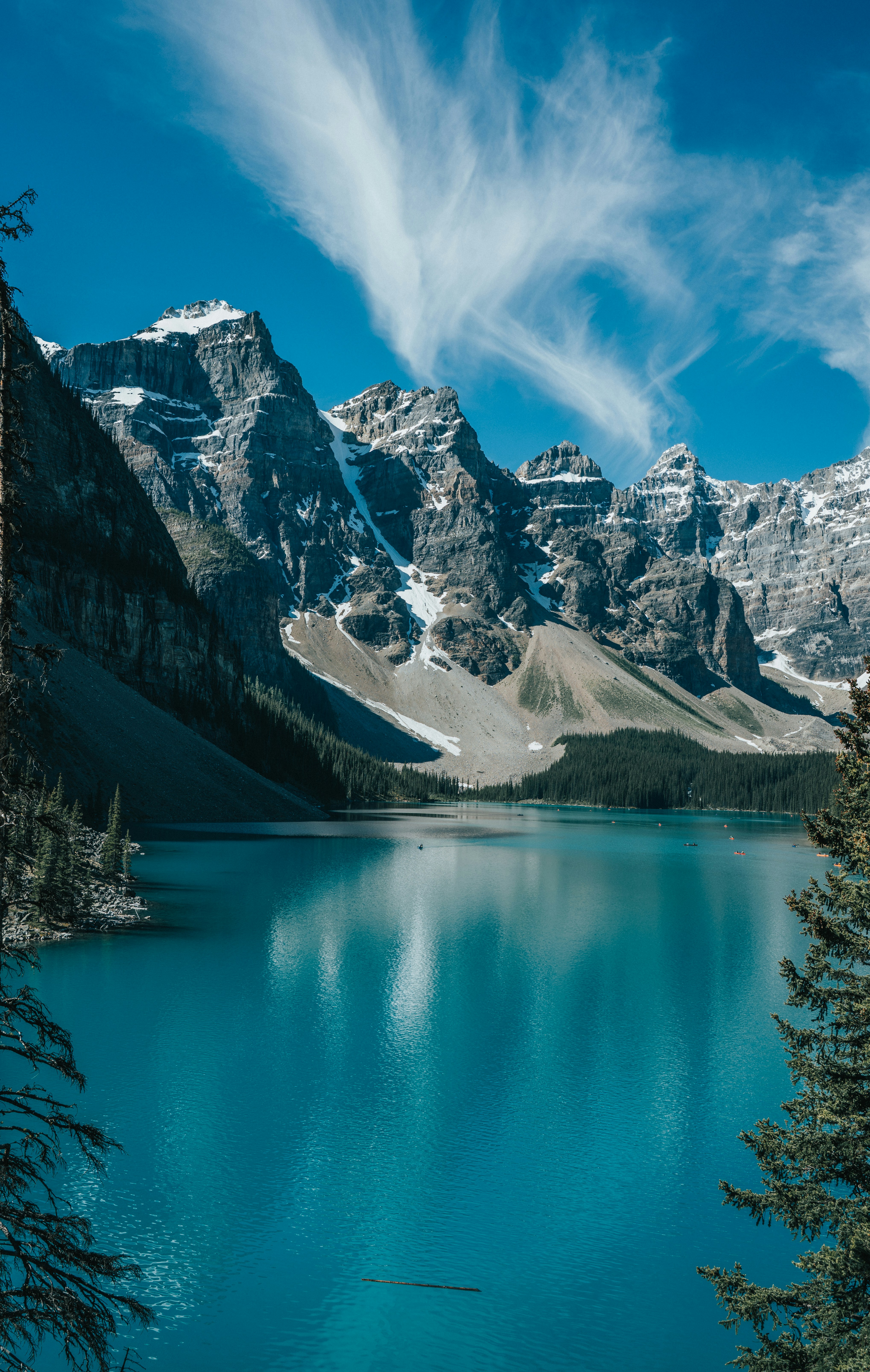 Turquoise lake reflects snow-capped mountains under blue sky.