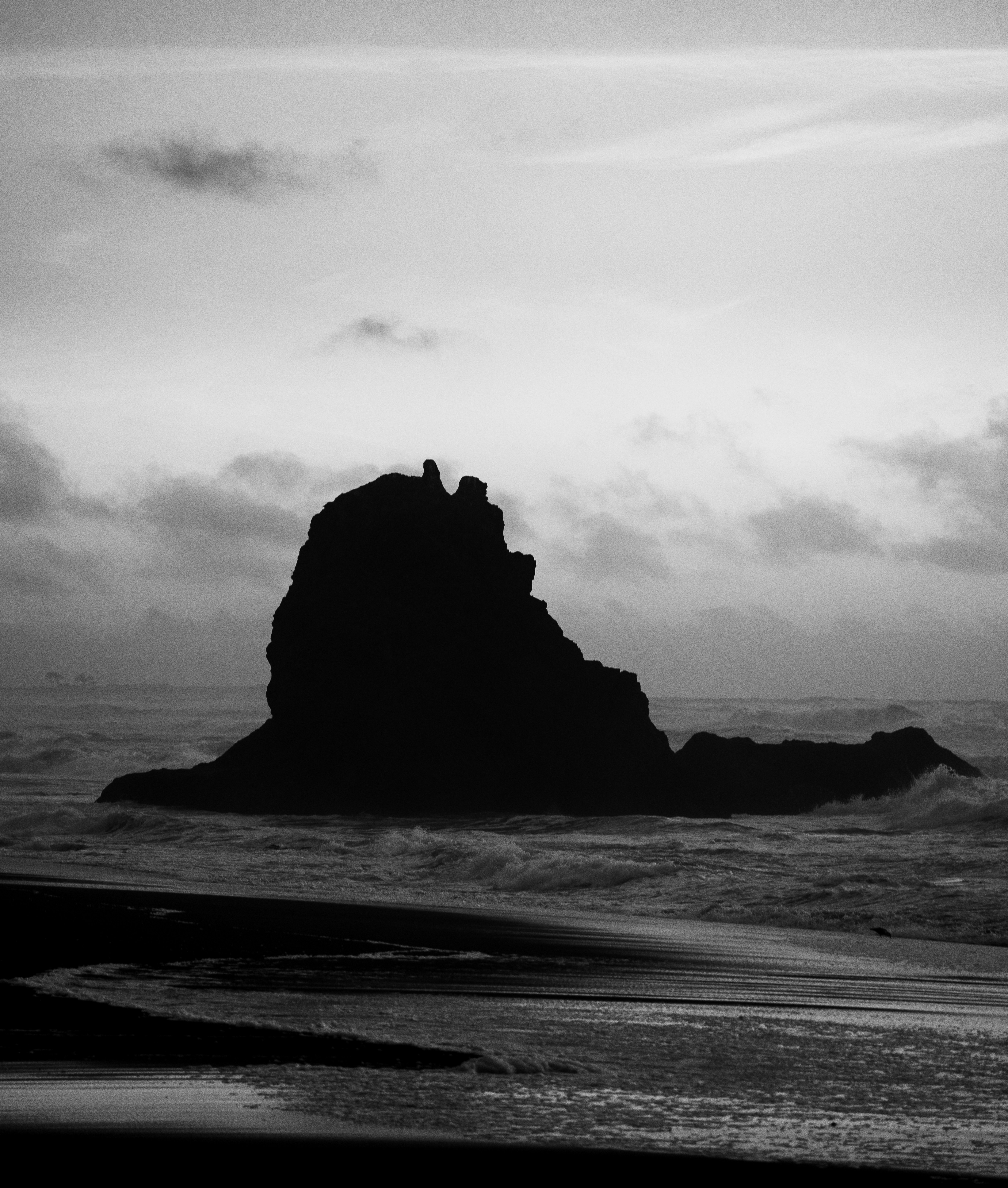 Silhouette of a large rock formation on a stormy beach.