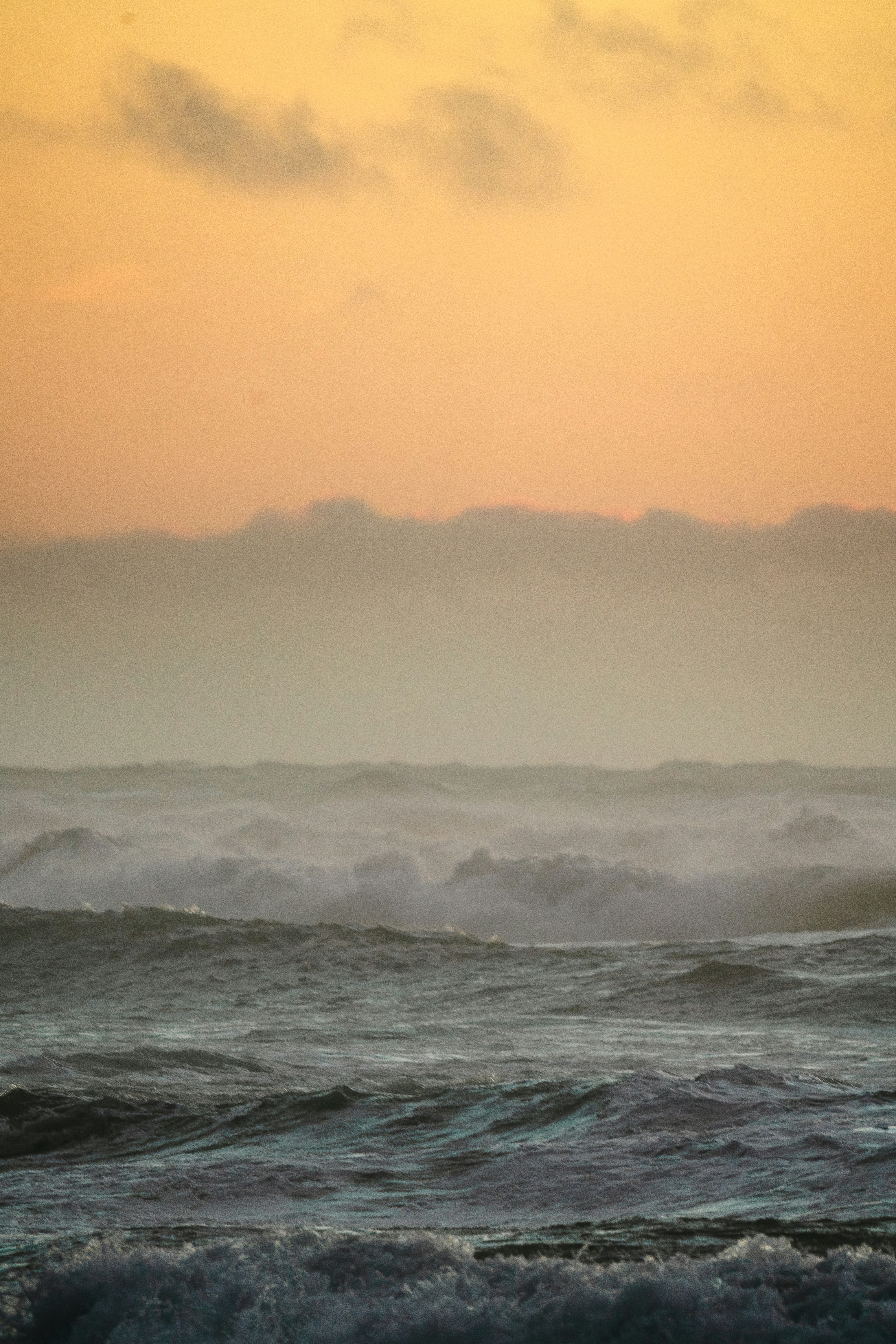 Waves crash on the shore under a hazy sky.