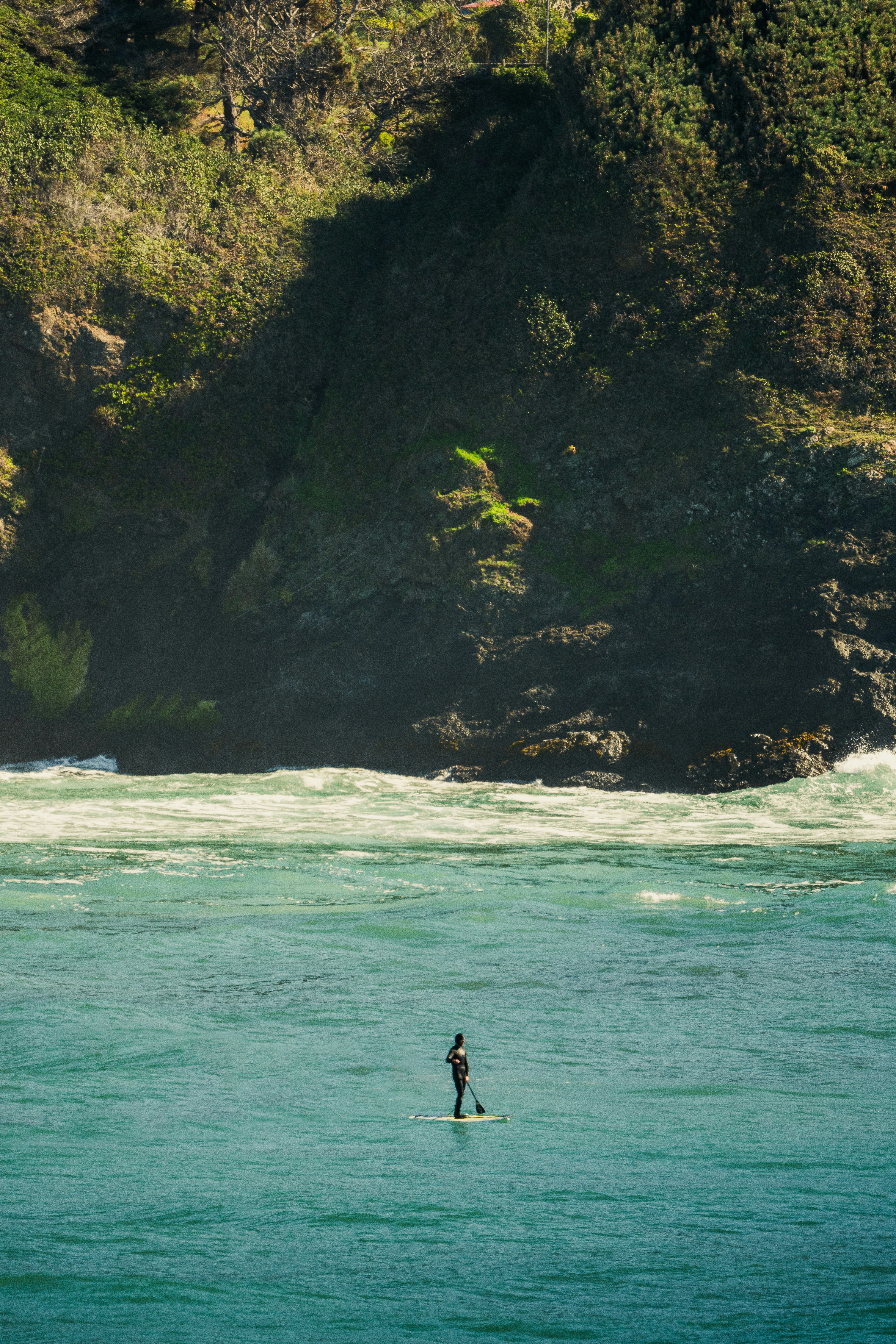A lone surfer stands on a paddleboard in the ocean.