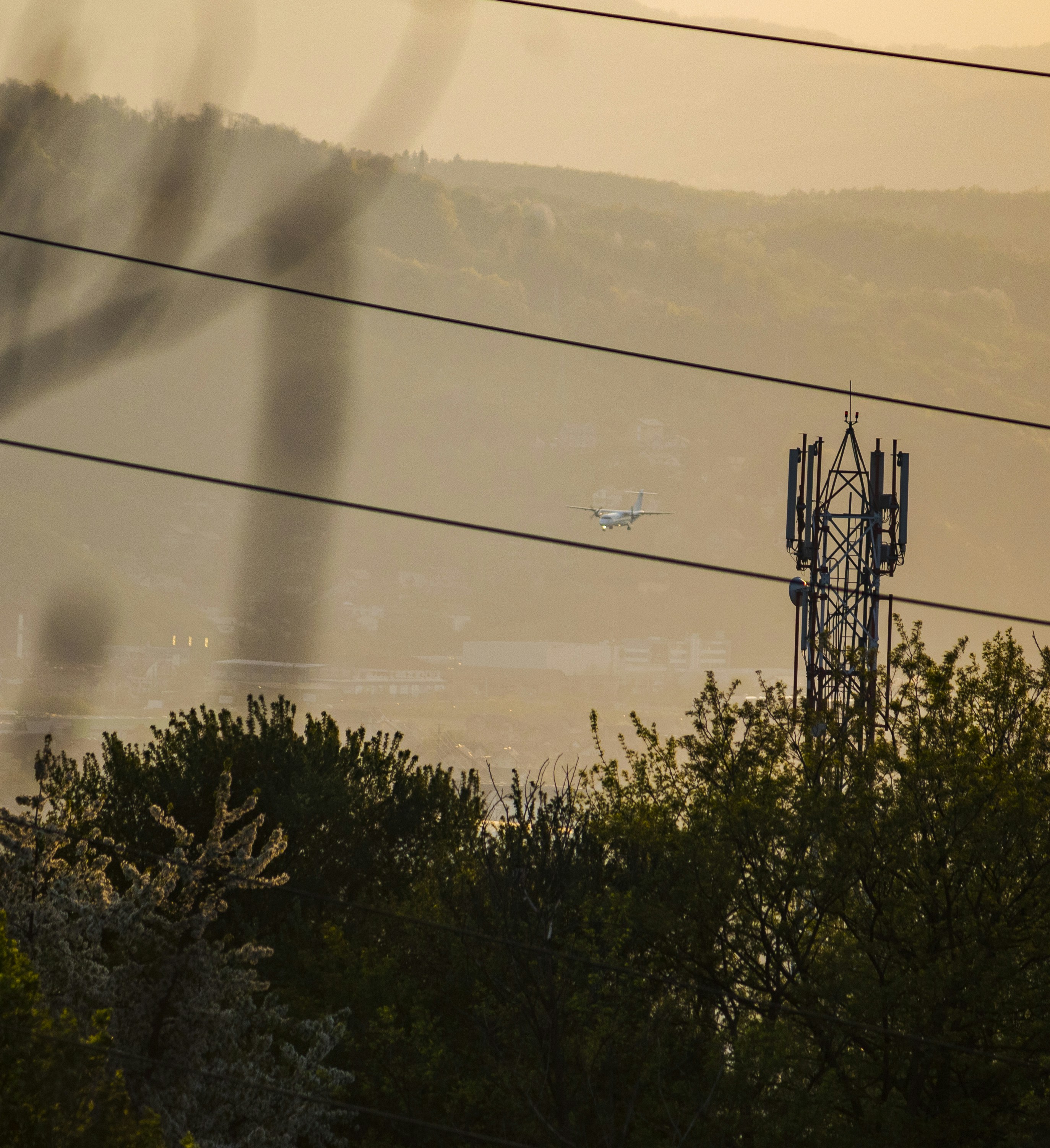 Airplane flying past cell tower at sunset