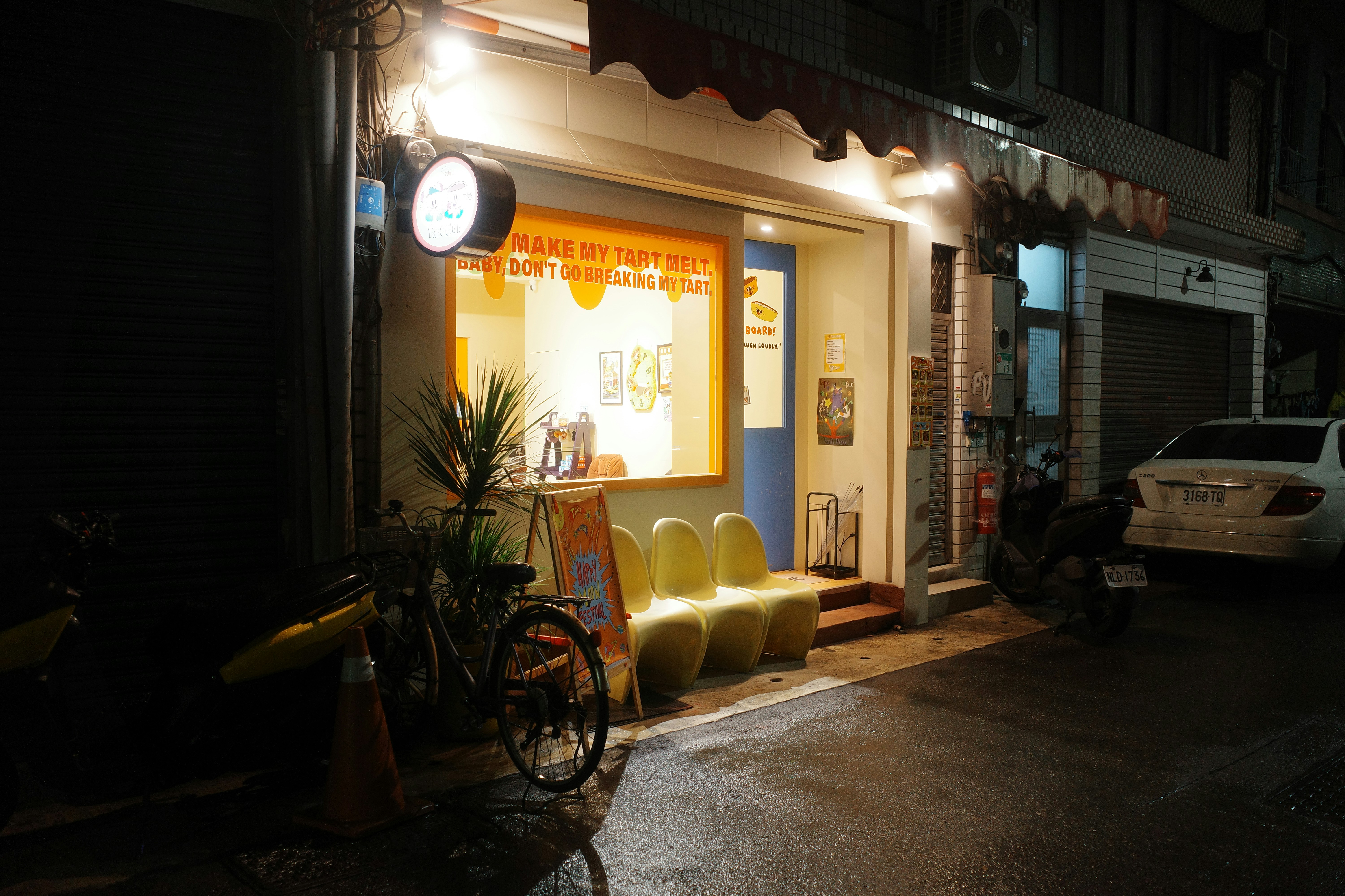 A brightly lit storefront at night with a yellow bench.